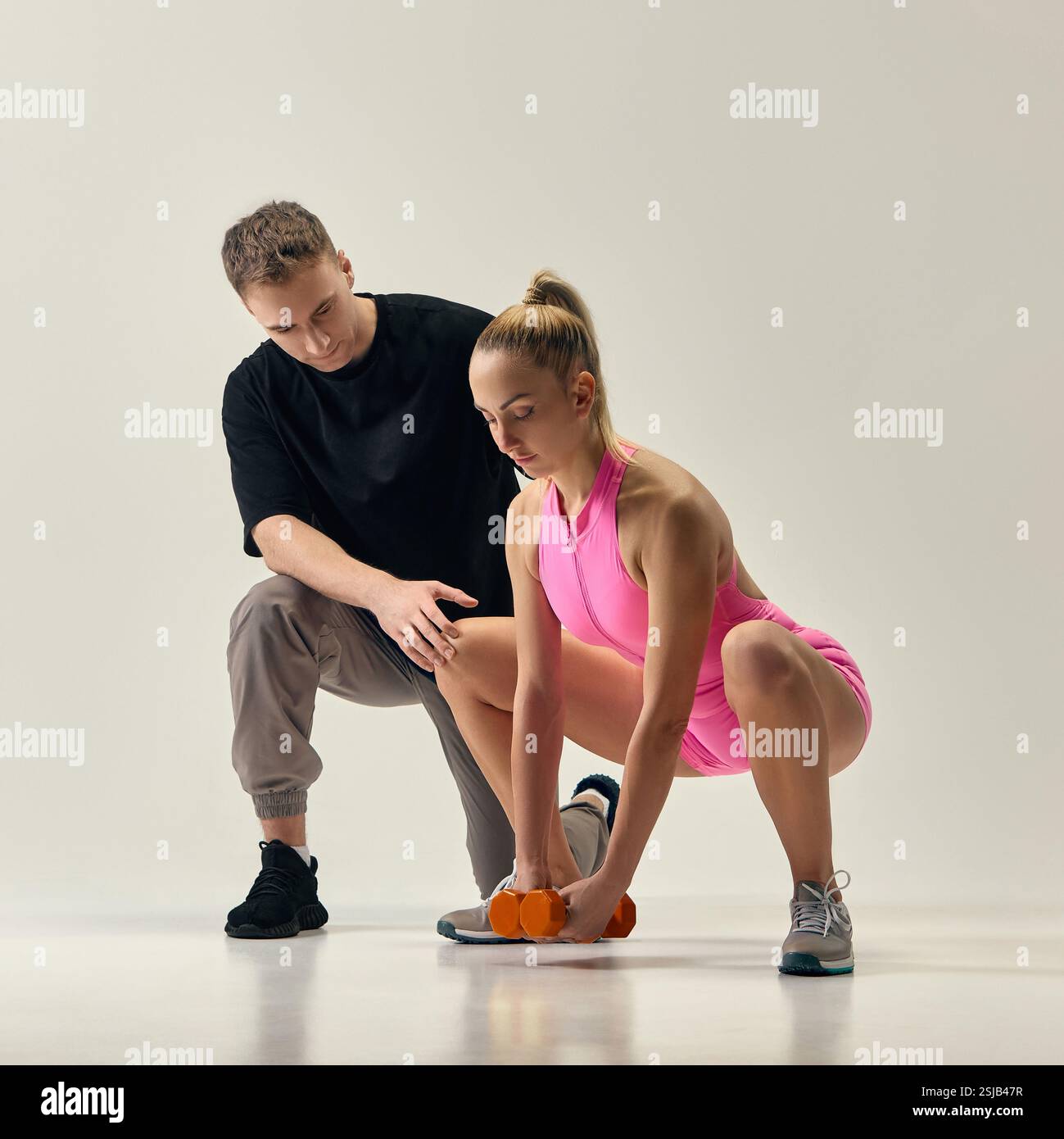 Trainer guides woman doing squat with dumbbells, ensuring proper ...