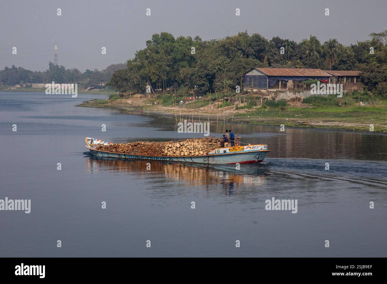 A small cargo vessel, heavily loaded with wood, makes its way through ...