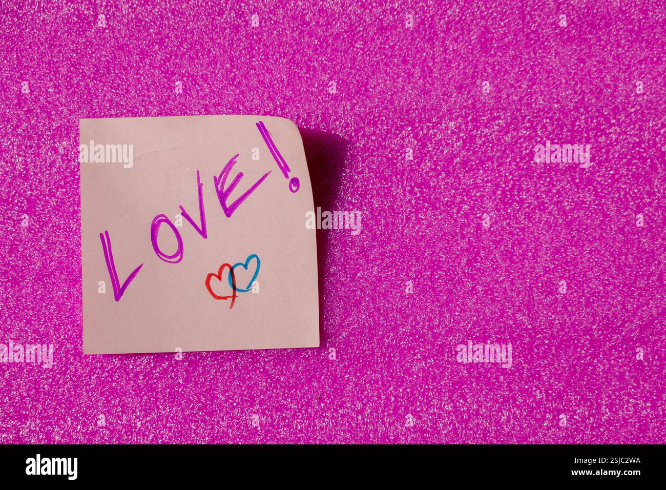 'Love' handwritten on a sticky note against a pastel pink backdrop ...