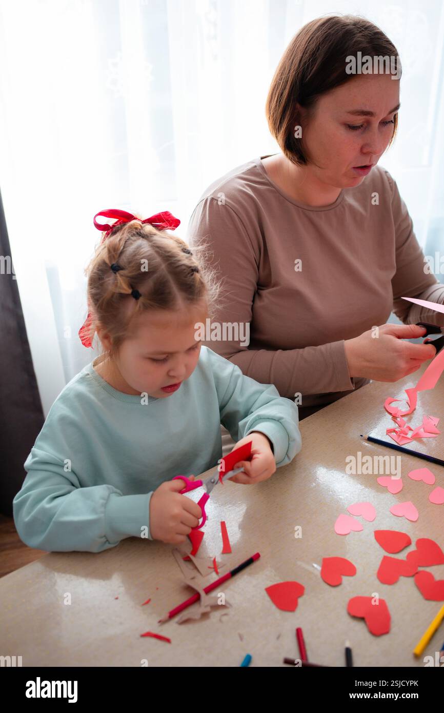 Portrait of little cute girl cut out paper hearts sitting at a desk ...