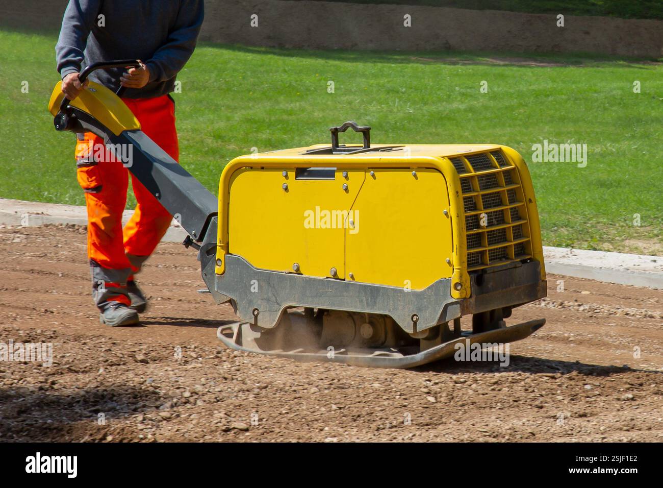A construction worker work-hardens a sandy ground with a vibratory ...