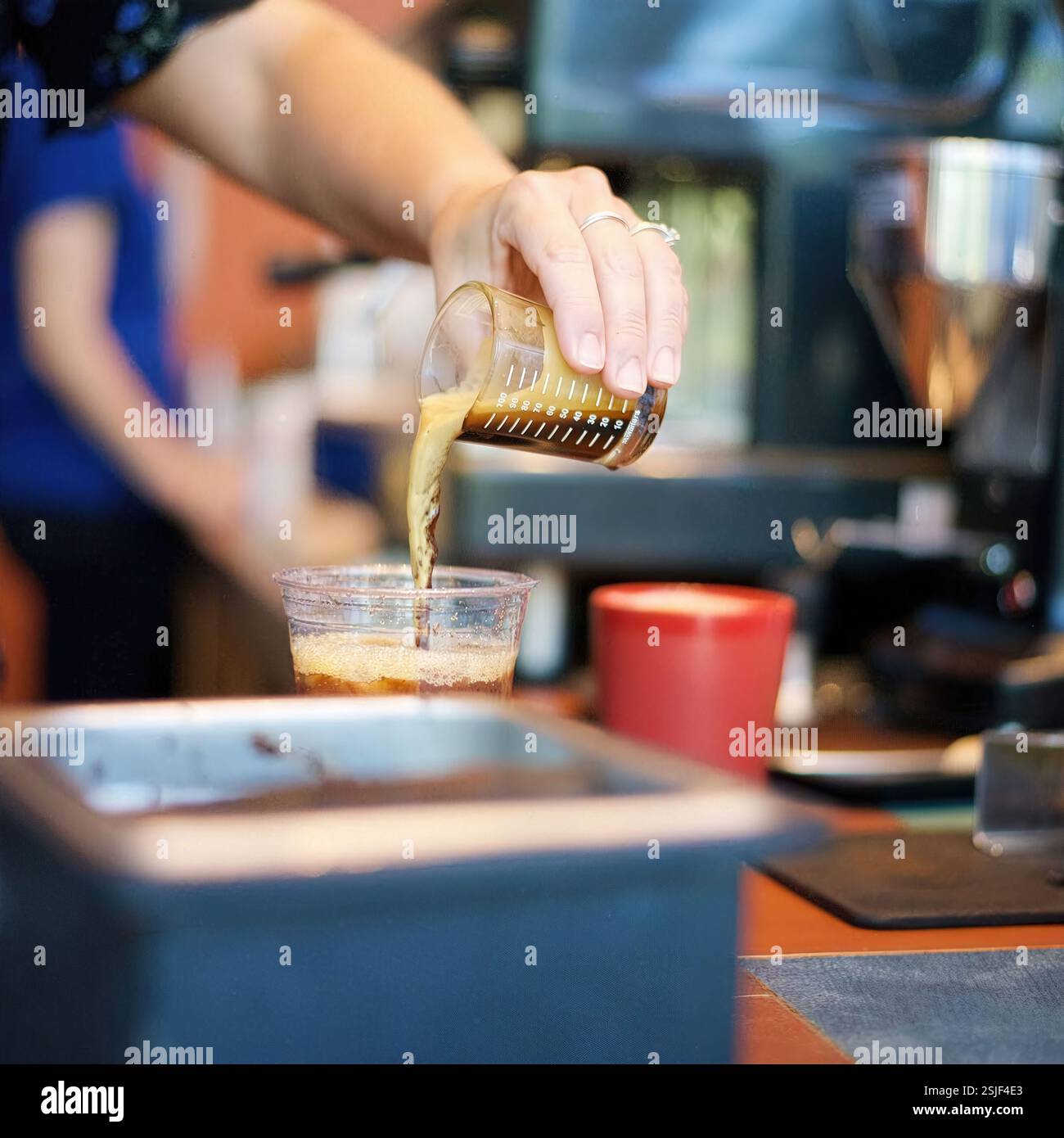 Barista pours espresso shot into iced coffee at a busy café counter ...