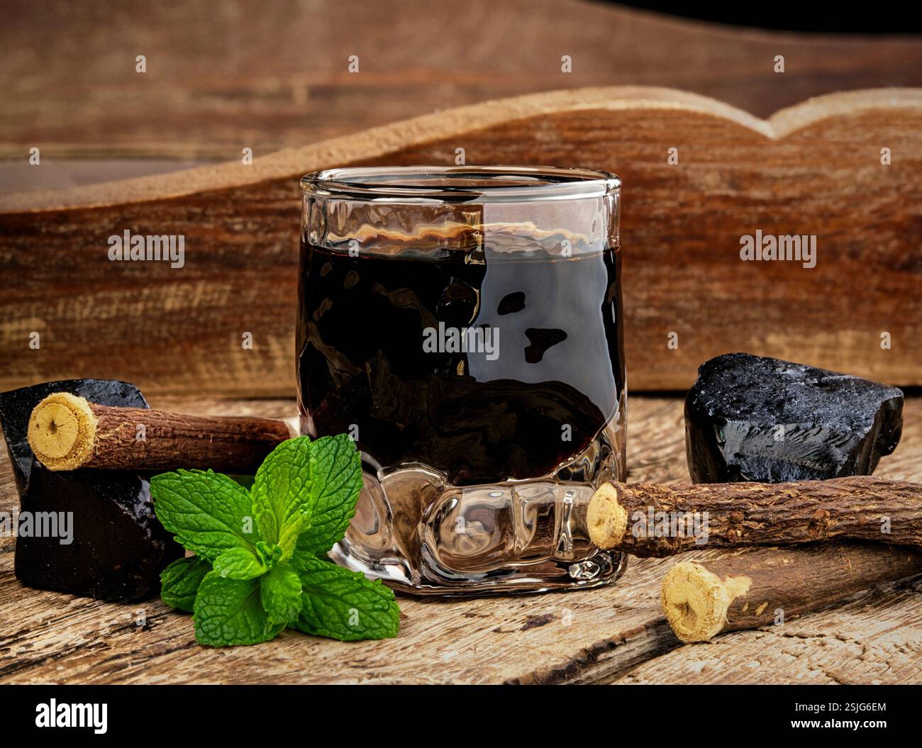 Licorice liqueur with pure blocks, root and fresh mint on wooden table ...