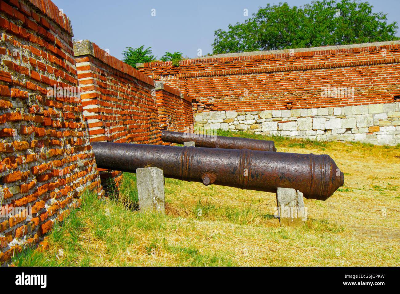 Two old cannons sit on stone bases against aged brick walls in a ...