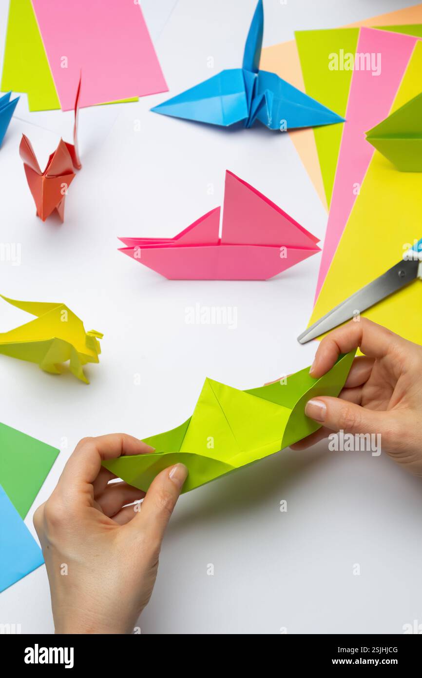 Woman's hands folding origami colored paper on table. Hobby, handmade ...