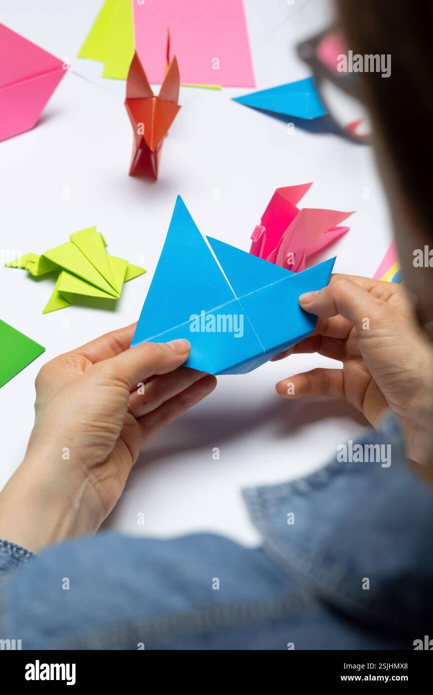 Woman's hands folding origami colored paper on table. Hobby, handmade ...