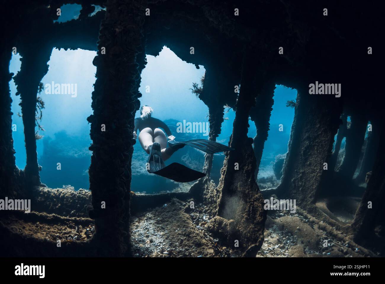 Freediver explores underwater shipwreck, surrounded by light rays and ...