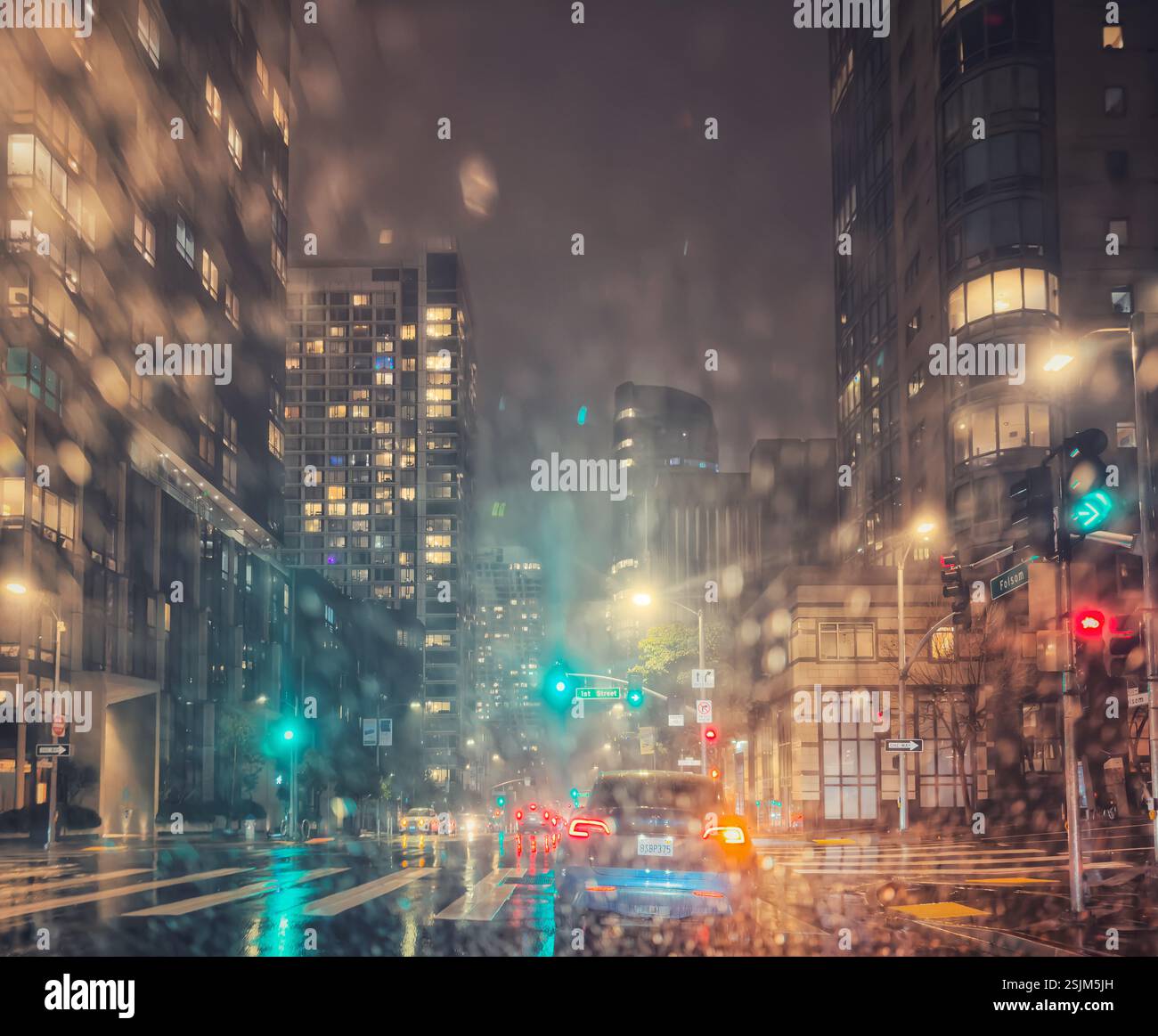 The image captures a nighttime cityscape view through a rain-streaked ...