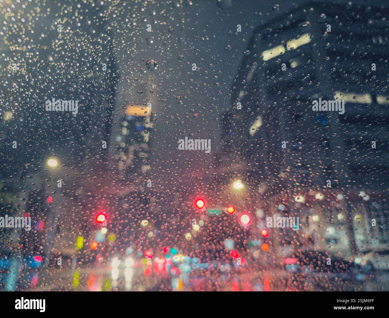 The image captures a nighttime cityscape view through a rain-streaked ...