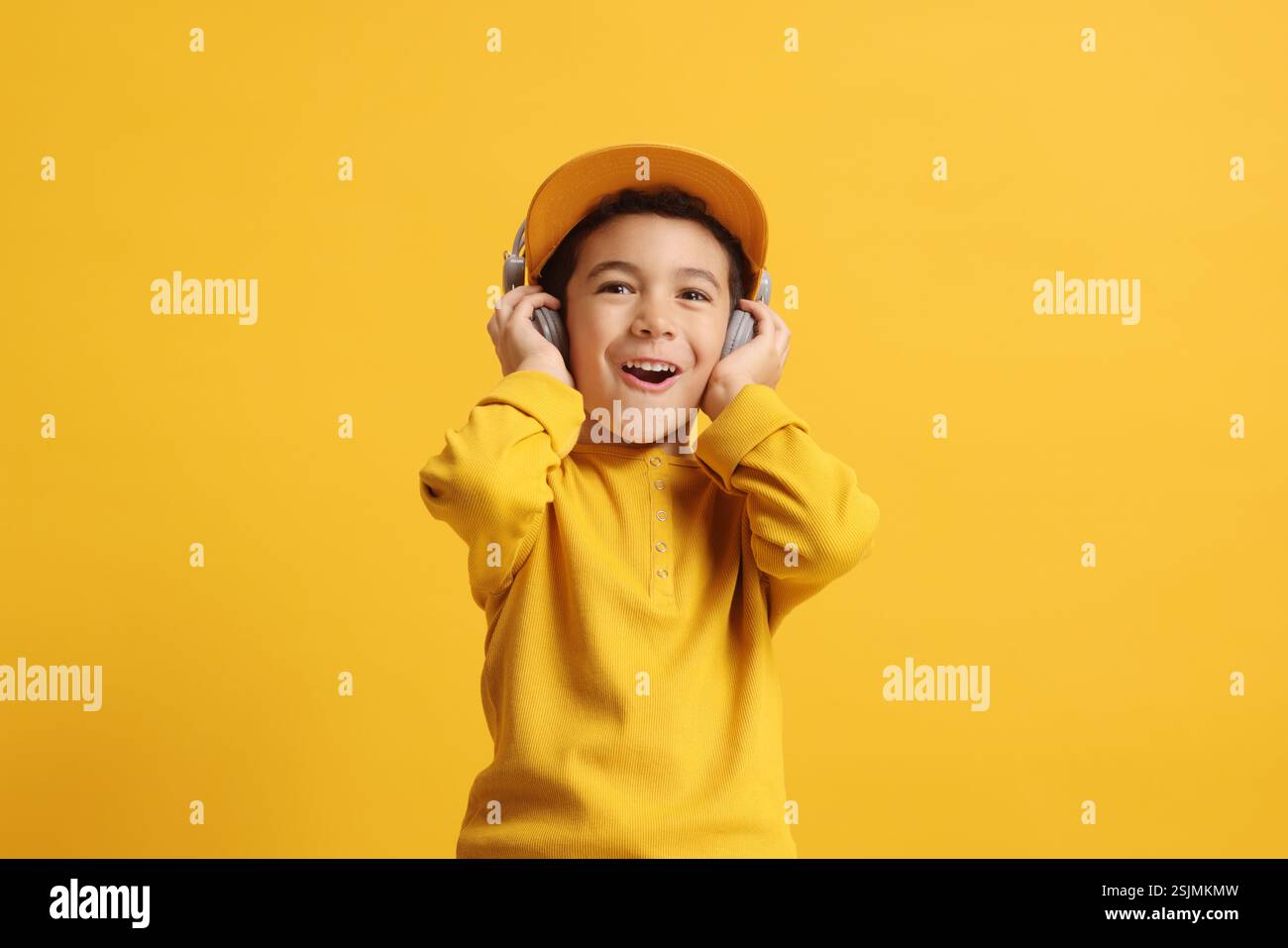 Kid with a cap and headphones listening to music against a yellow ...
