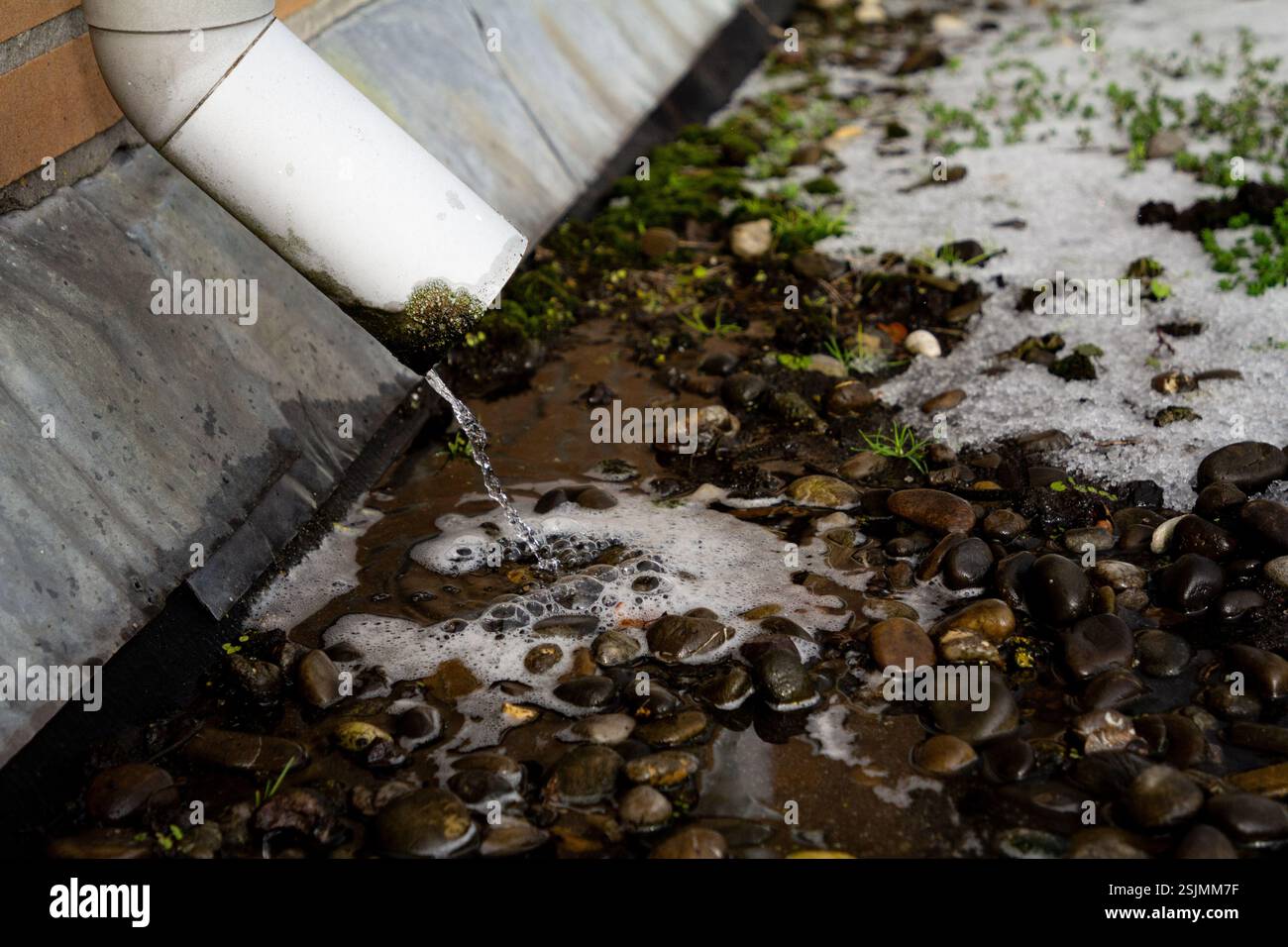 A close-up of a pipe attached to the roof, collecting water as snow ...