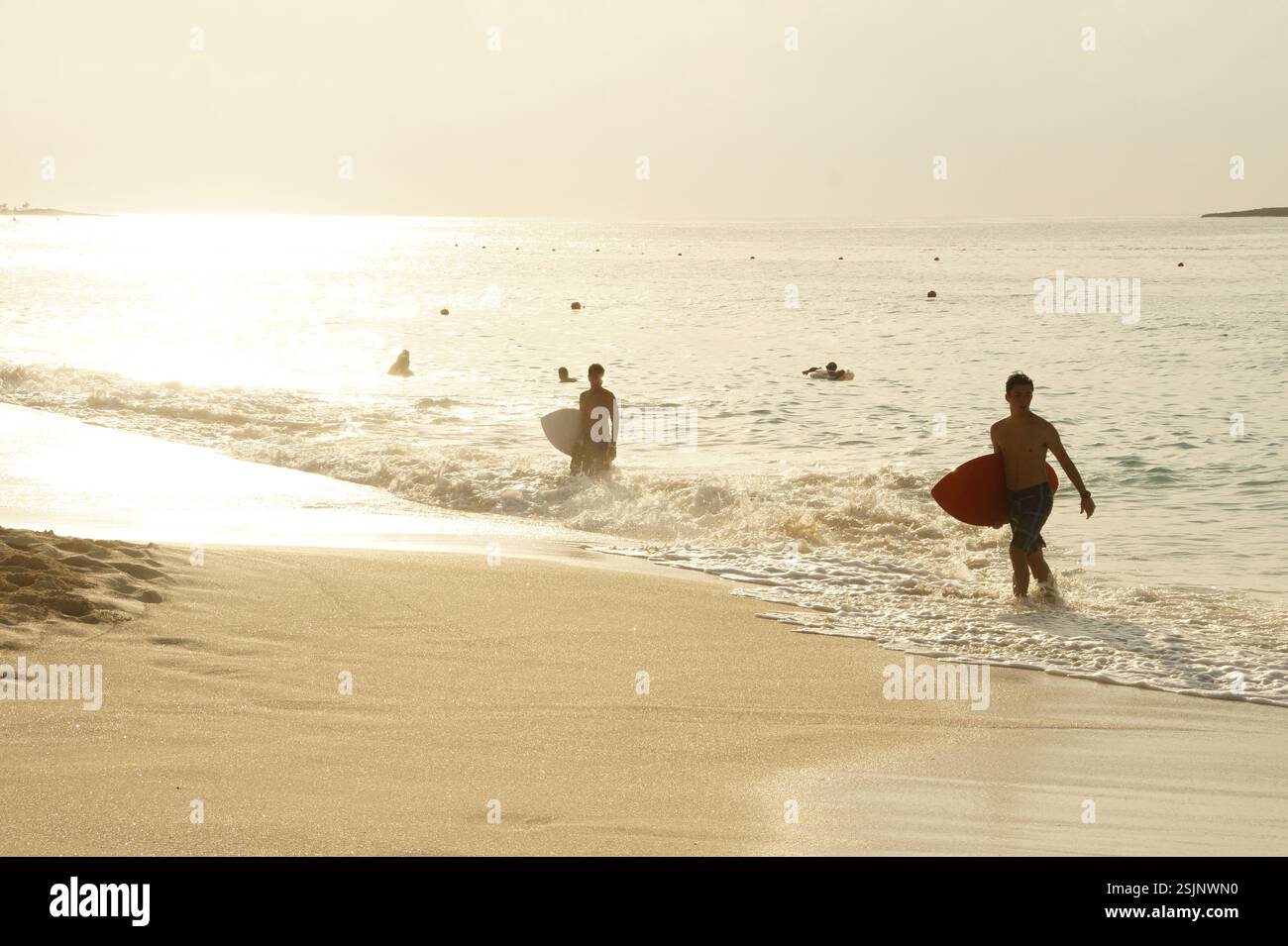 Surfers ride the waves, their silhouettes painted against a ...