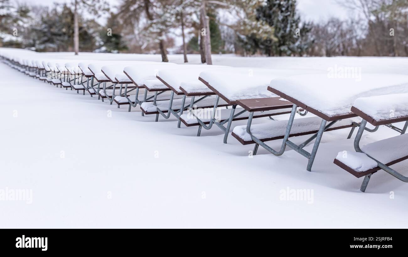 Photo of snow-covered stacked picnic tables in a park during the winter ...
