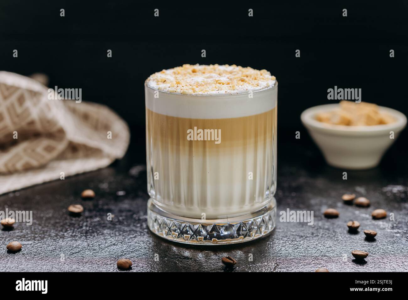 Layered latte with frothy milk and crushed nuts in crystal glass with ...