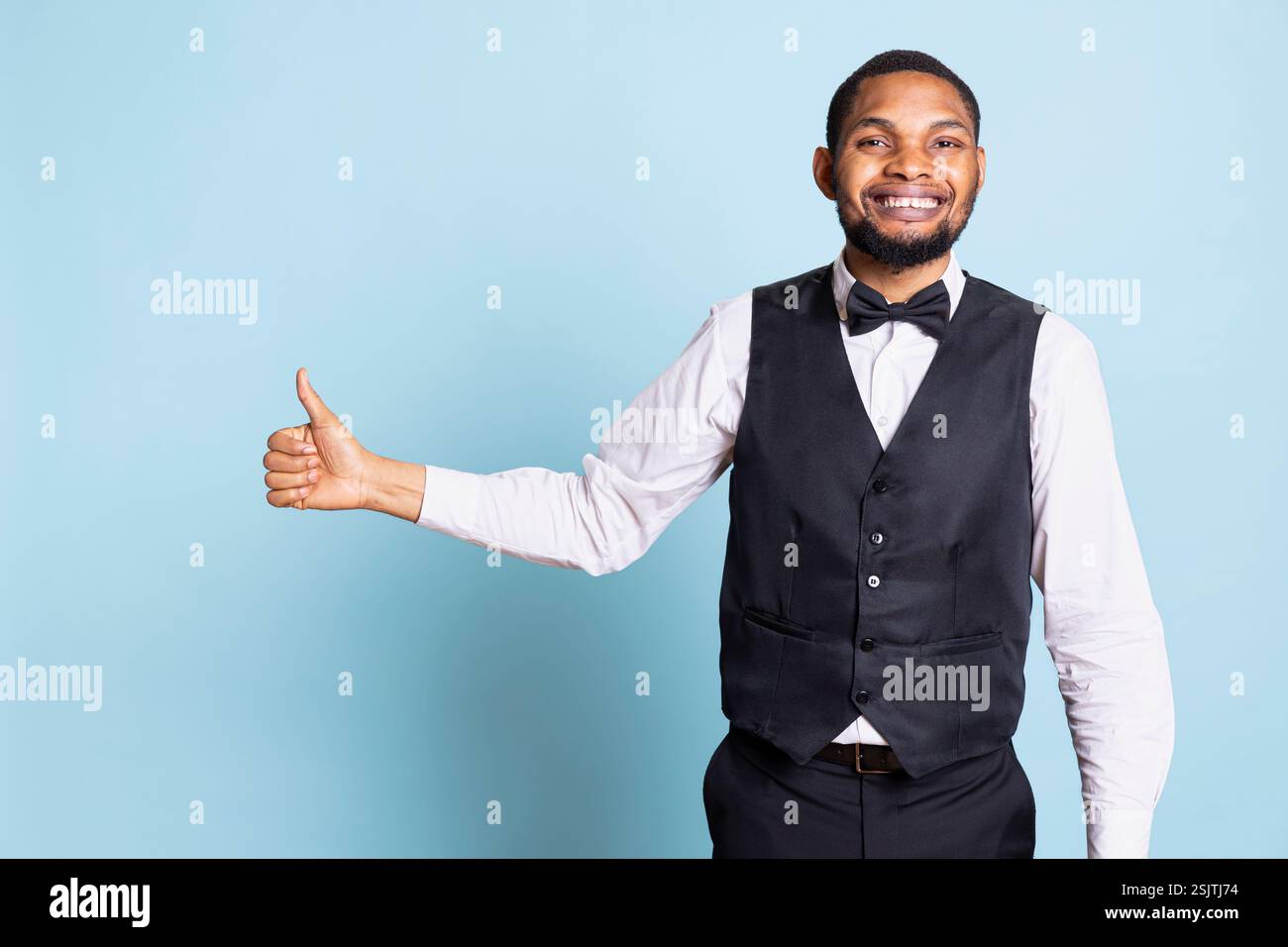 Smiling bellboy in suit and tie showing thumbs up gesture in studio ...