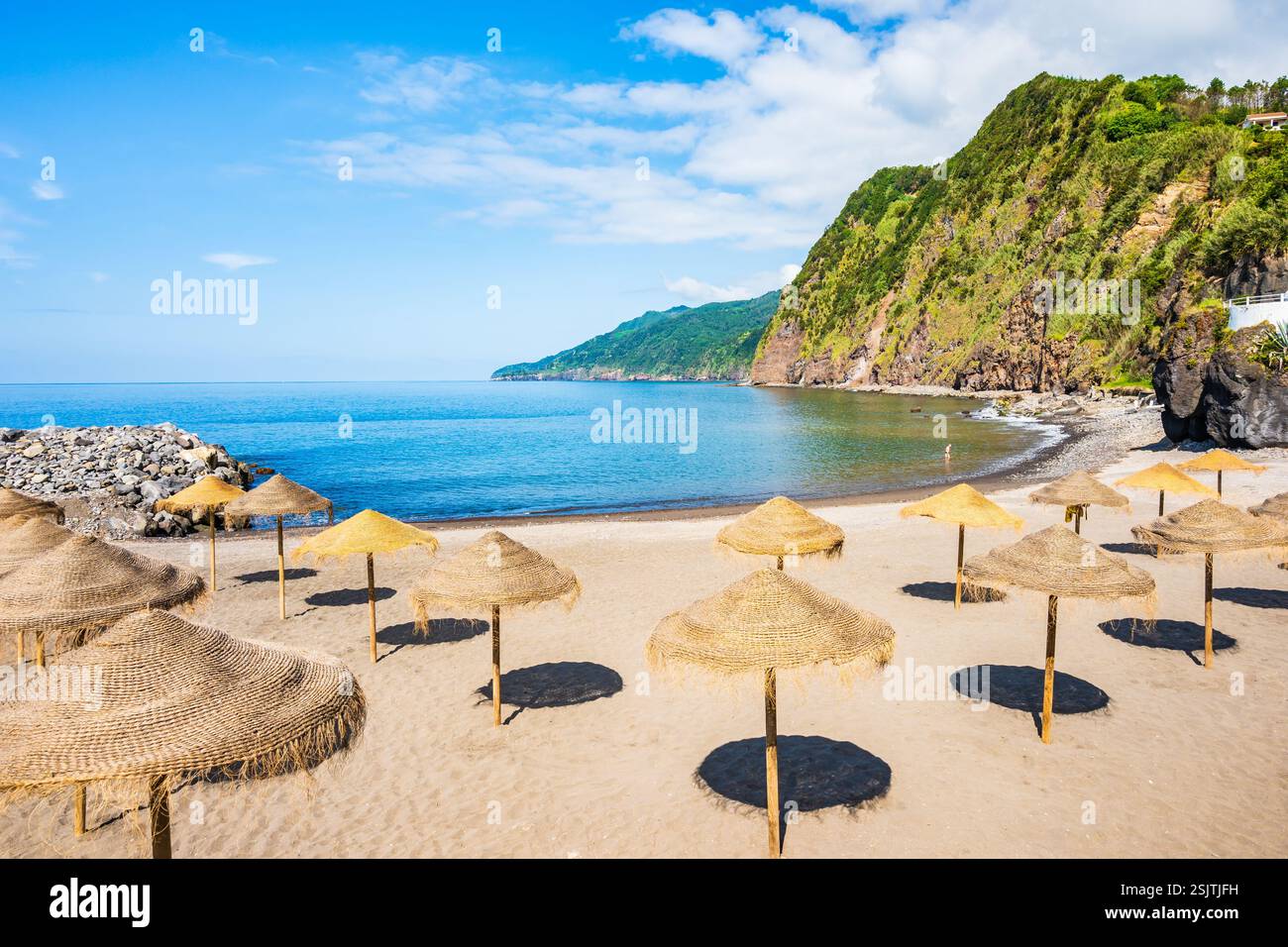 Sun umbrellas on beach in Povoacao town and green hills in background ...