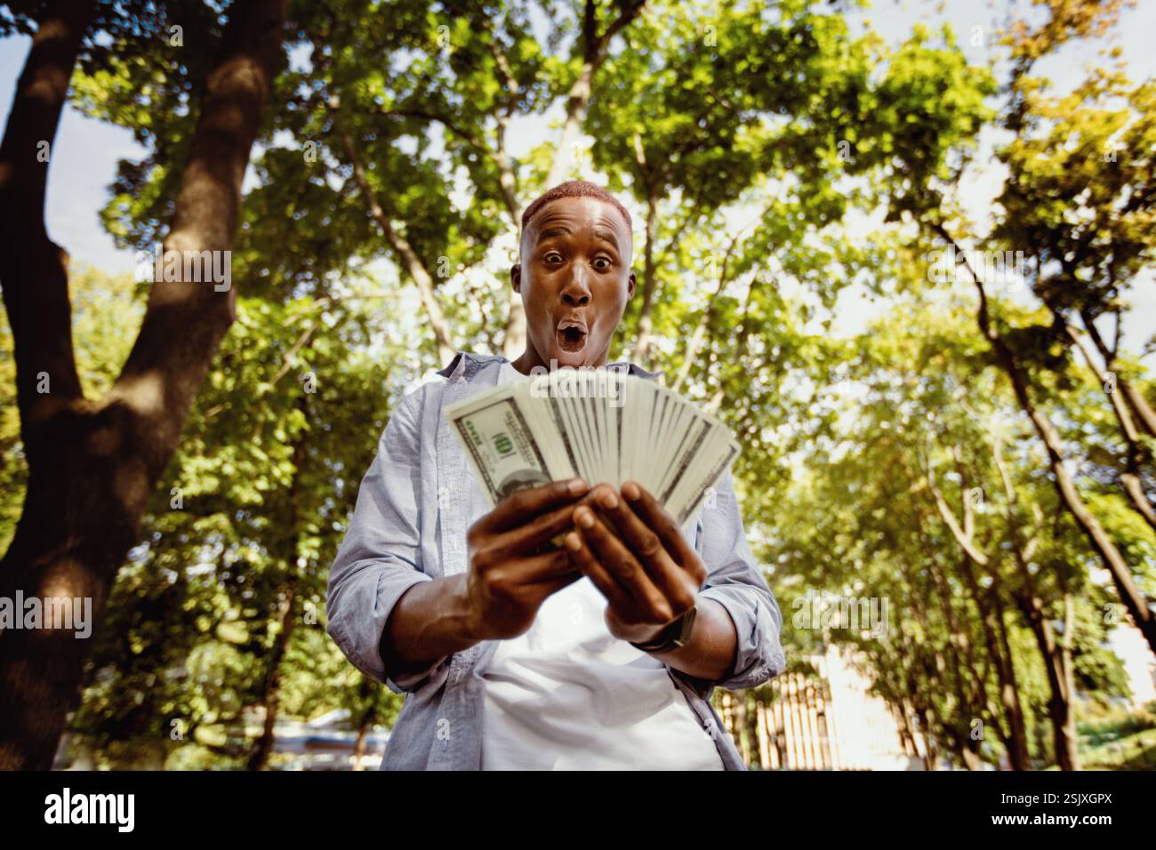 Shocked black man with huge fan of money at city park Stock Photo - Alamy