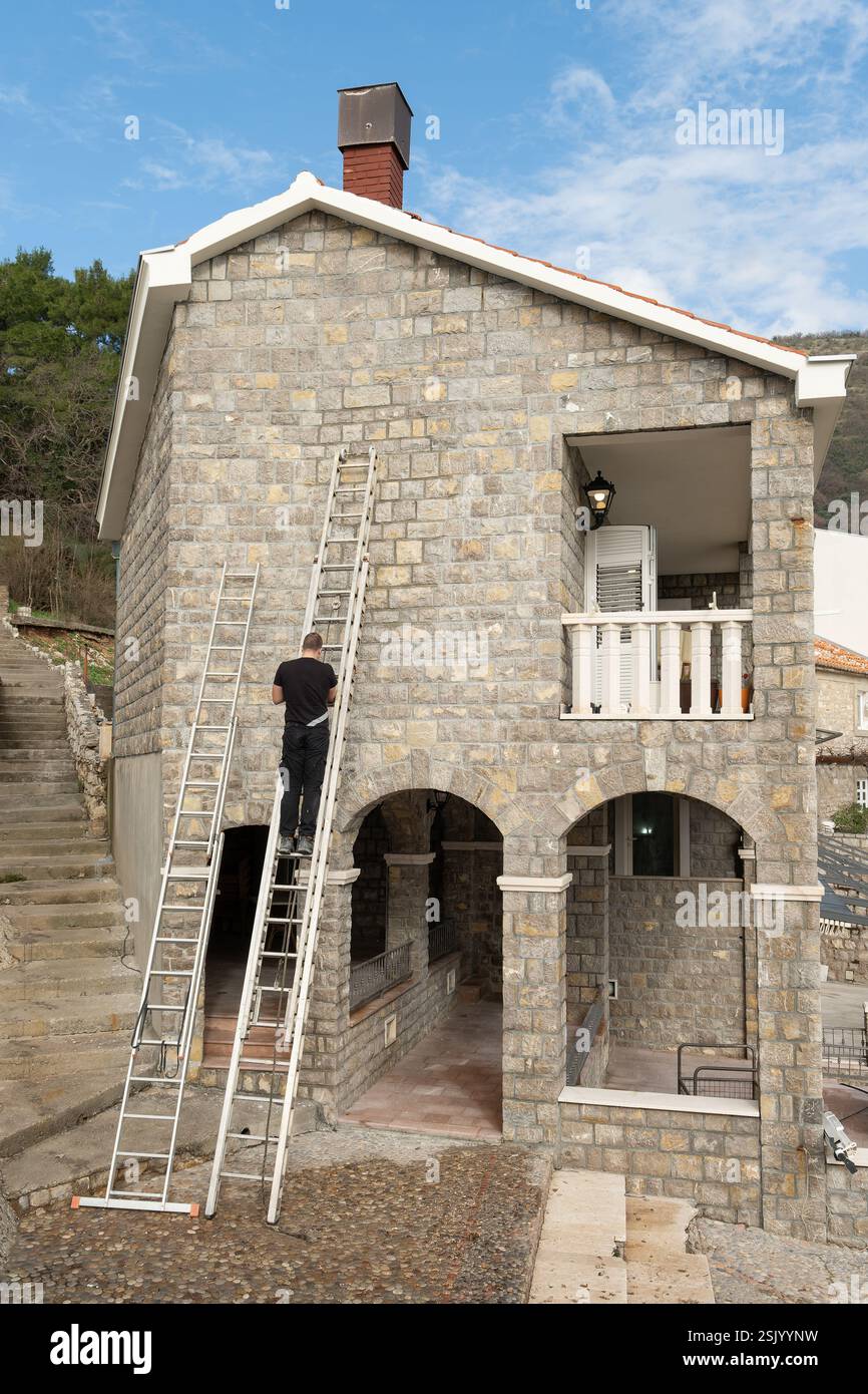 Worker on ladder repairing facade of an old Mediterranean stone house ...