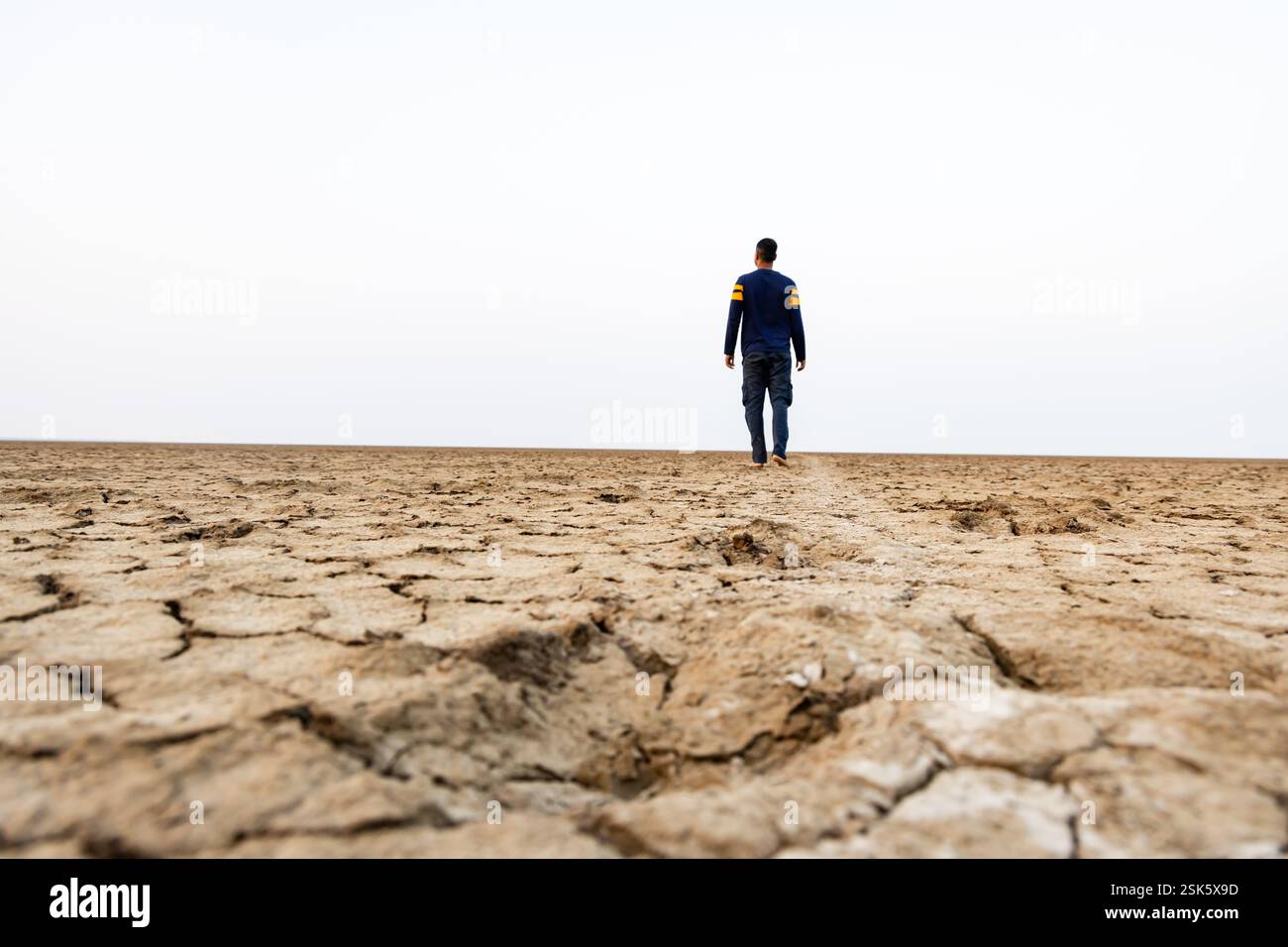 farmer standing at dry cracked farm fields focus to blur from low angle ...