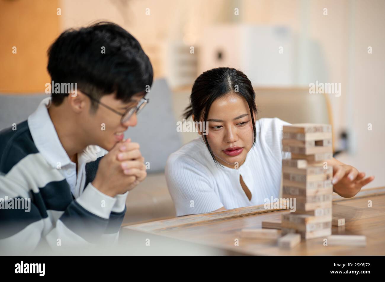 Two cheerful Asian friends, a male and a female, enjoy playing Jenga ...