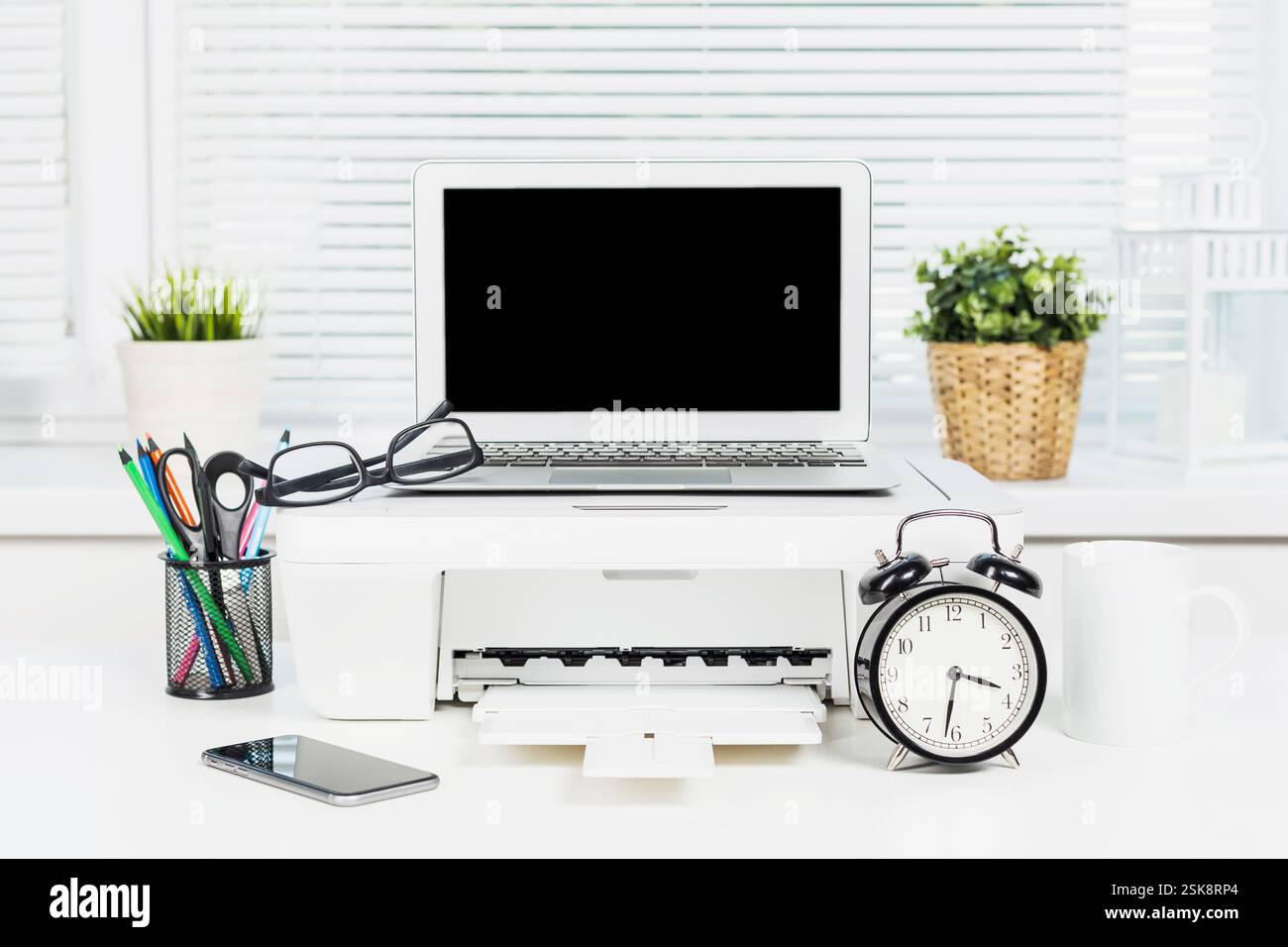 Desk setup with laptop, printer, and office supplies during daytime in ...
