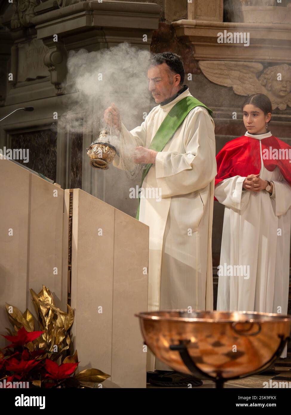 Cremona, Italy - February 9th 2025 Priest wearing white and green vestments swinging thurible ...