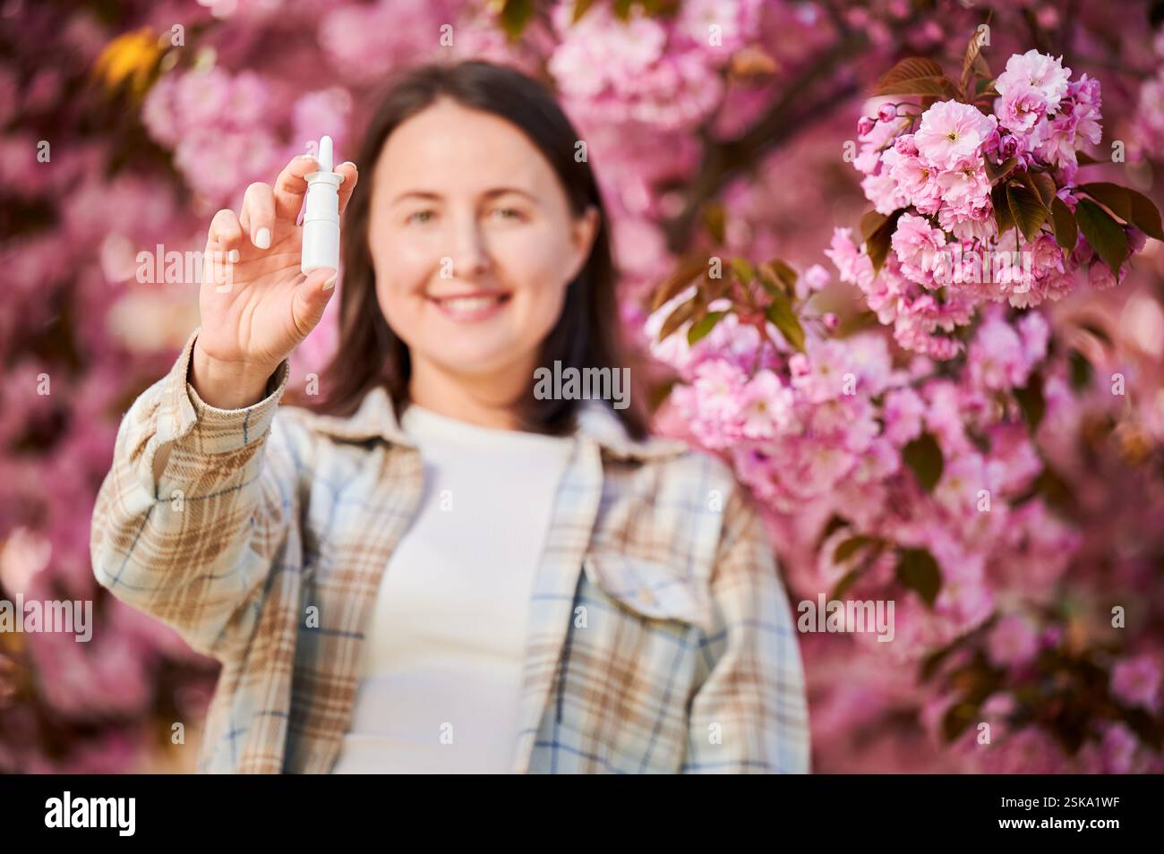Focus on woman hand's holding nasal spray. Smiling woman allergic using ...
