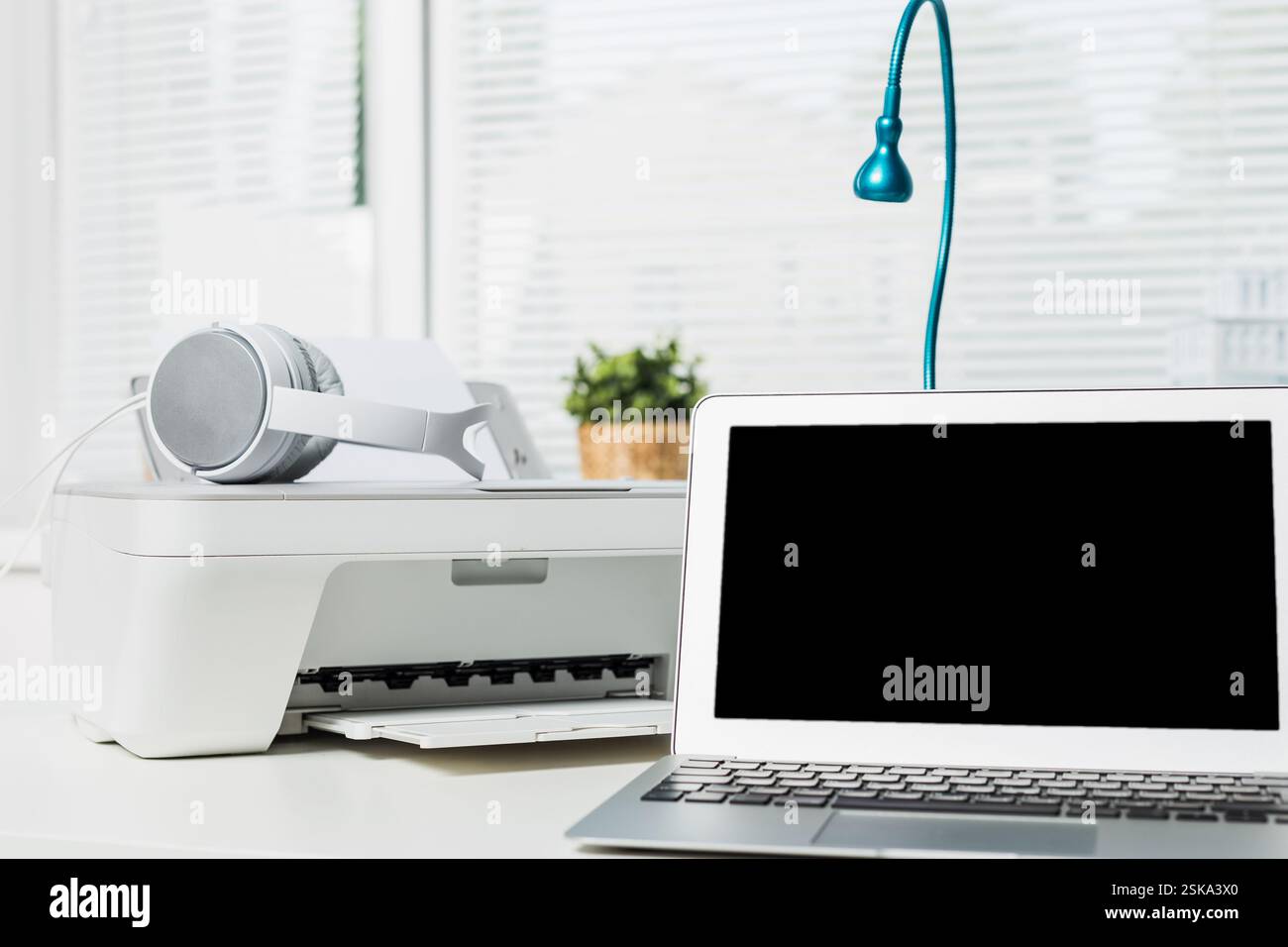 Work setup with desk, laptop, printer, and headphones in a bright room ...