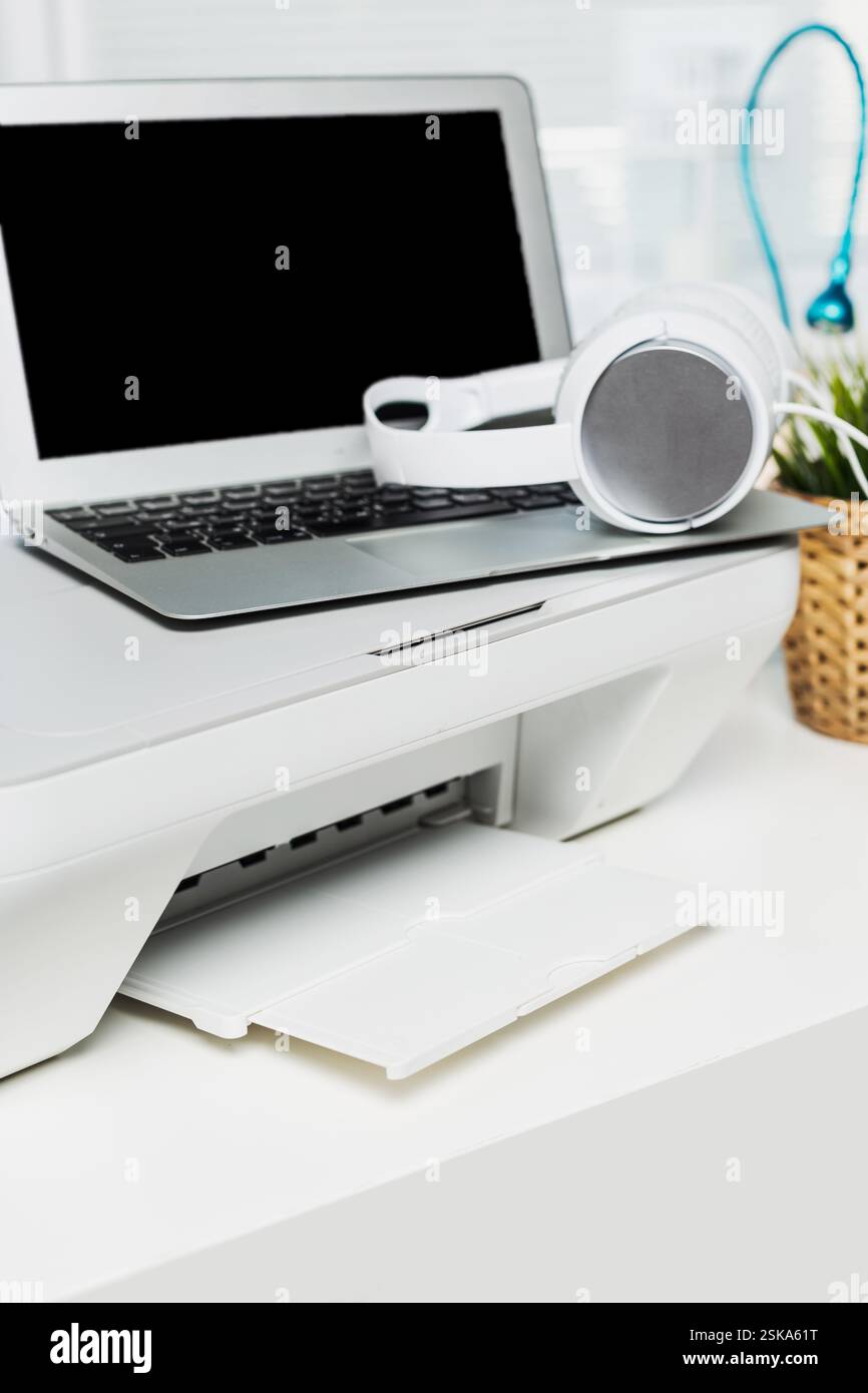 Modern workspace setup with laptop, printer, and headphones in a bright ...
