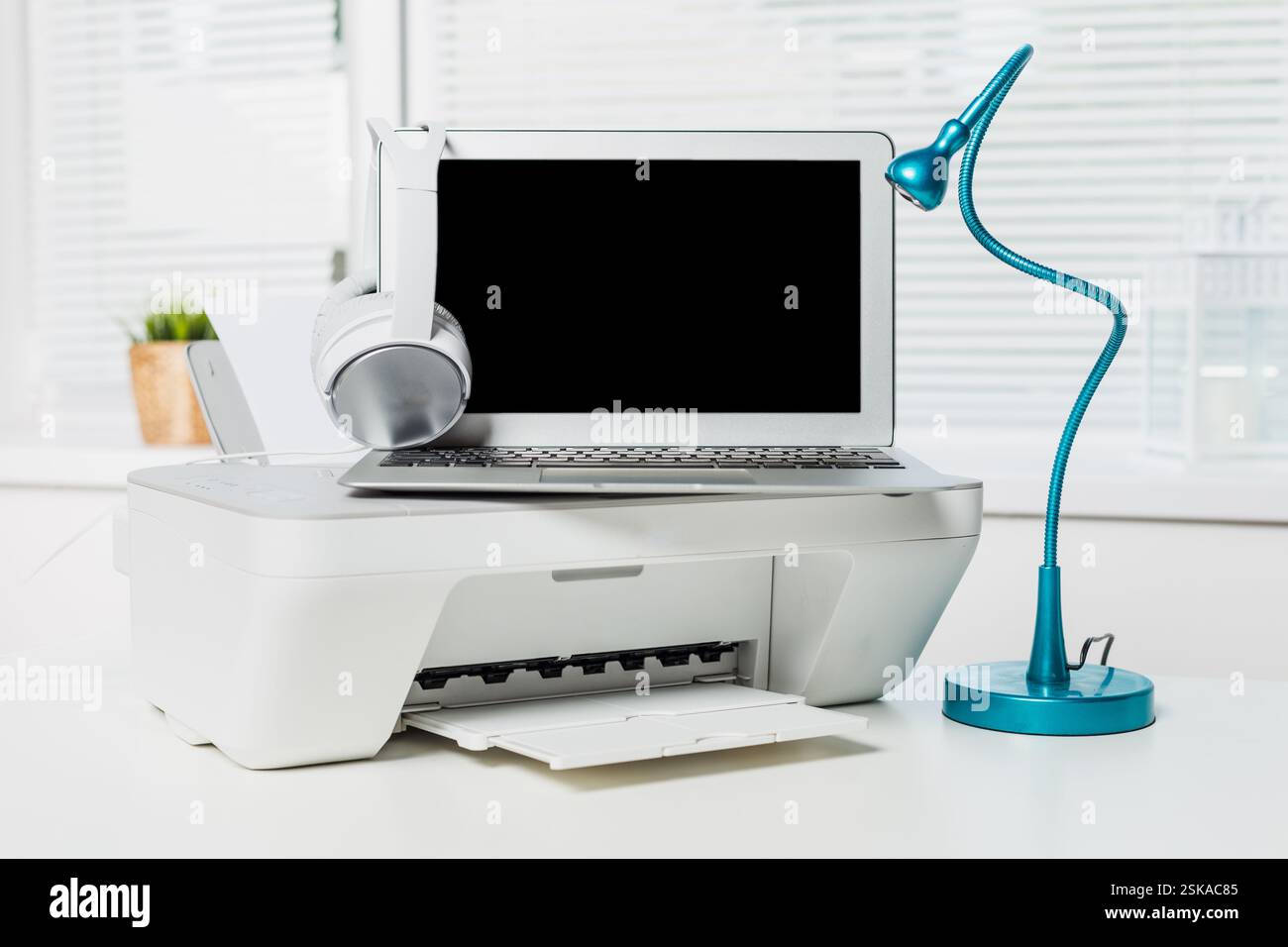 Modern workspace setup with laptop, printer, headphones, and desk lamp ...