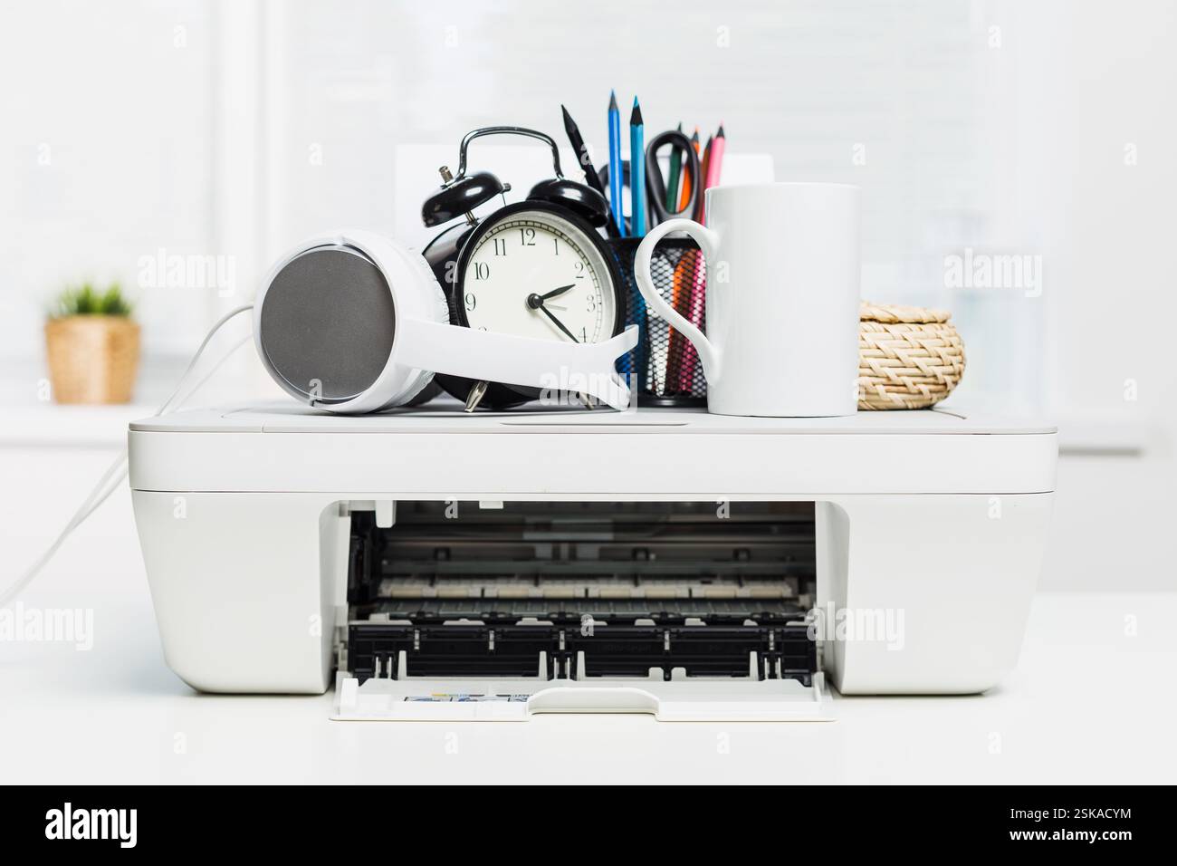 Office workspace with printer surrounded by stationery, clock, and cup ...