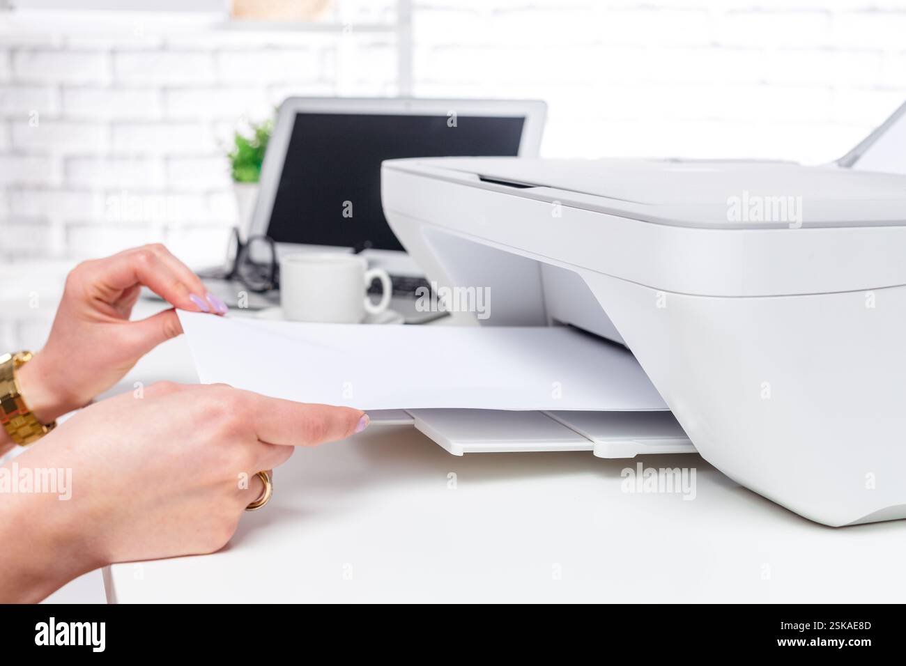 Hands placing paper into a modern printer at a bright workspace with a ...