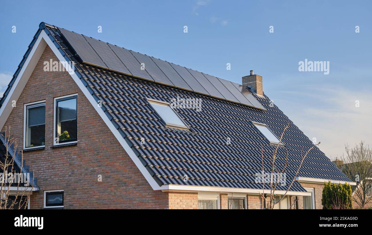 A residential house with black solar panels installed on a sloped tiled ...