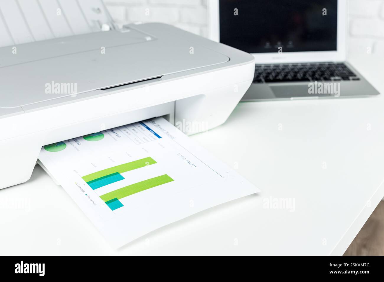 Printer producing document with color graphics beside a laptop on a ...