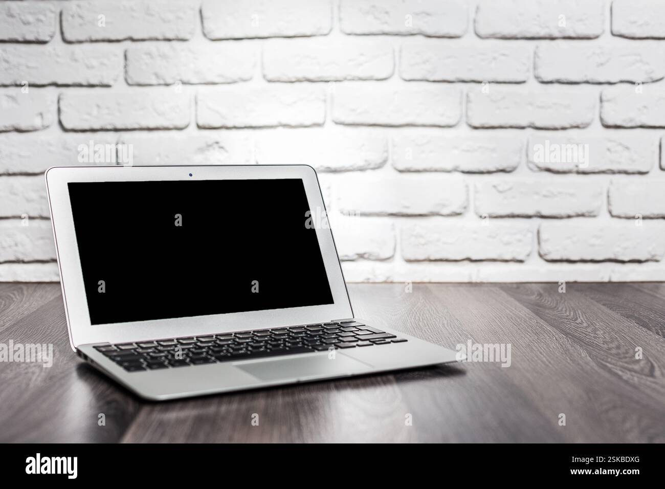 Sleek laptop placed on wooden table against a minimalist white brick ...
