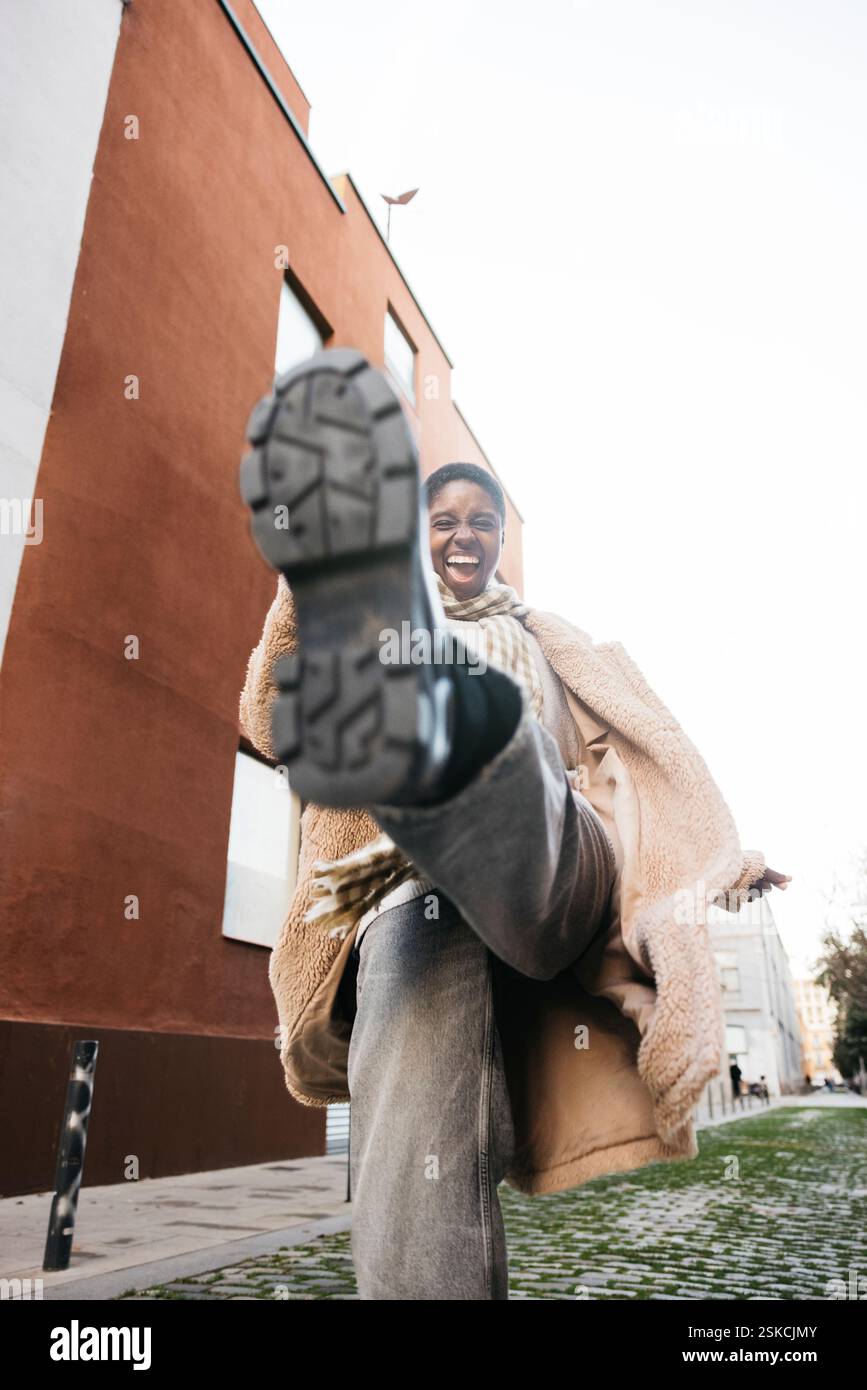Fashionable young woman playfully kicks her leg towards the camera ...