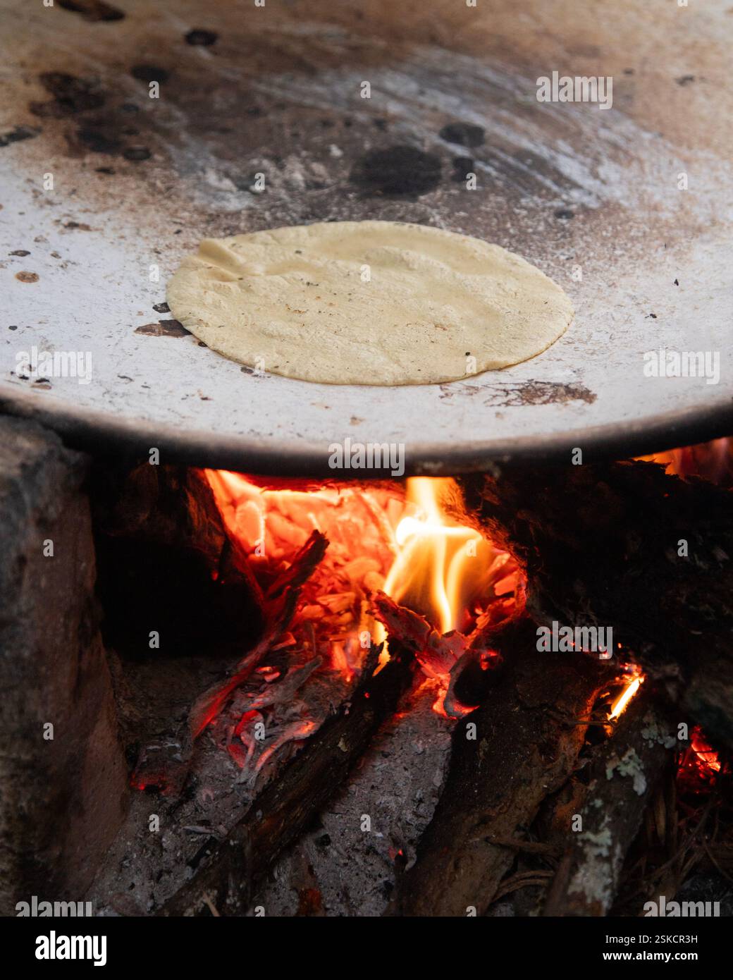 Cooking handmade corn tortillas on a traditional comal in an open fire ...
