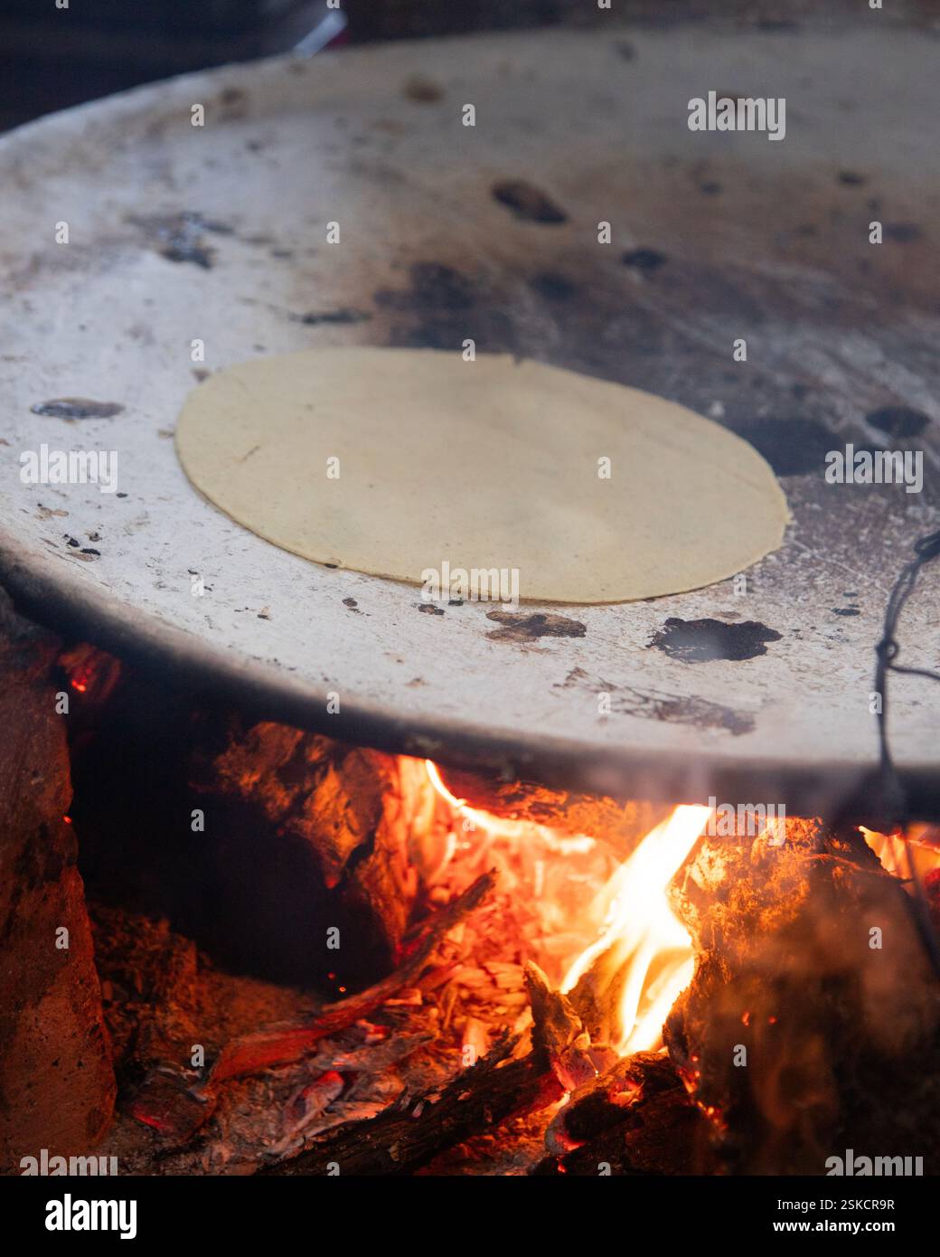 Cooking handmade corn tortillas on a traditional comal in an open fire ...
