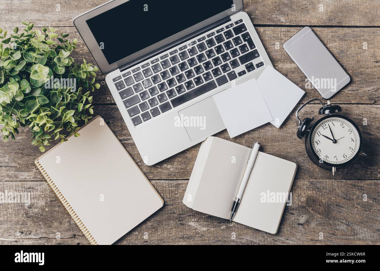 Workstation setup with laptop, clock, and notepads on wooden desk in a ...