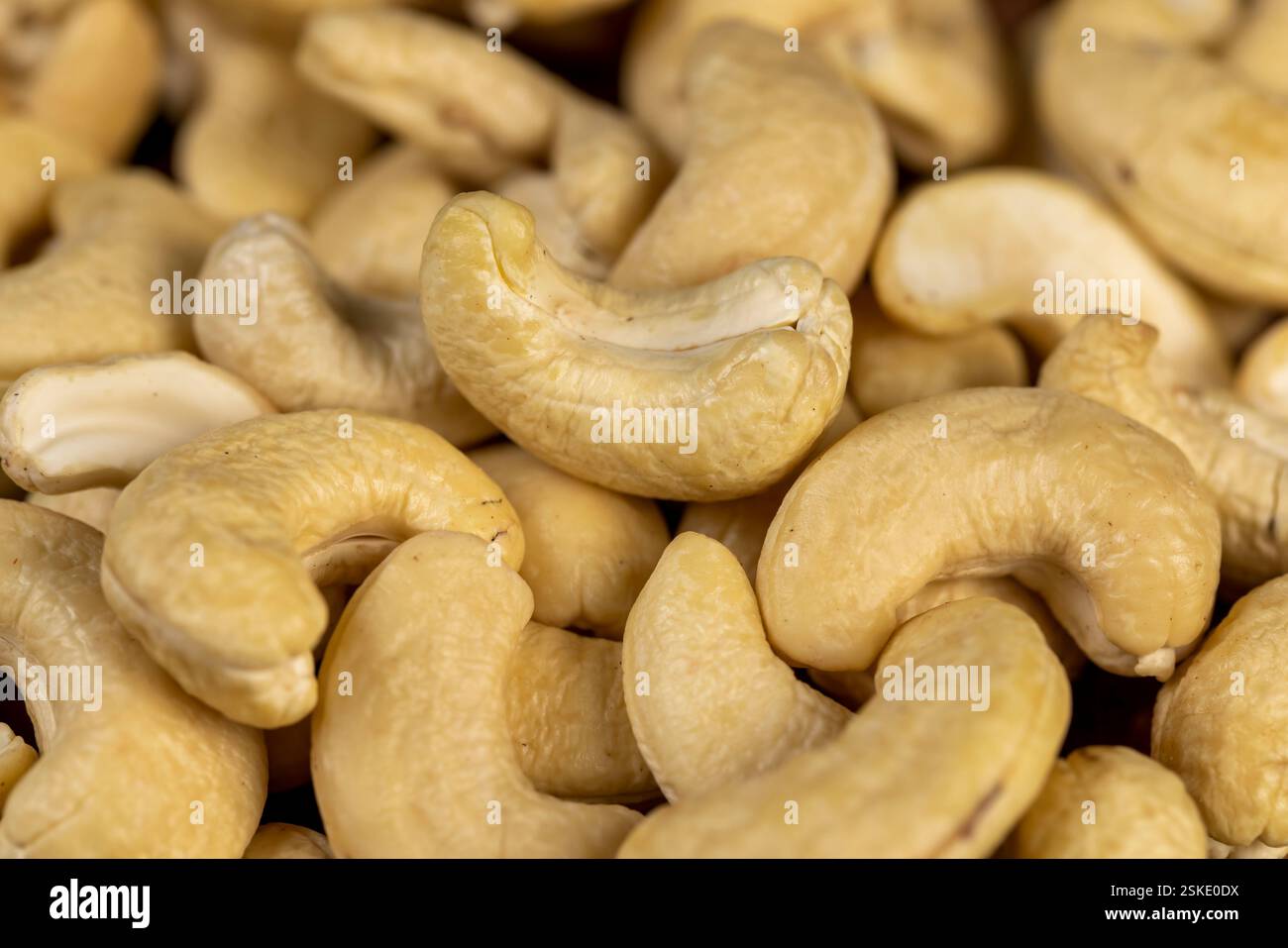 large cashew nuts are scattered on a larch board, raw unroasted cashew ...