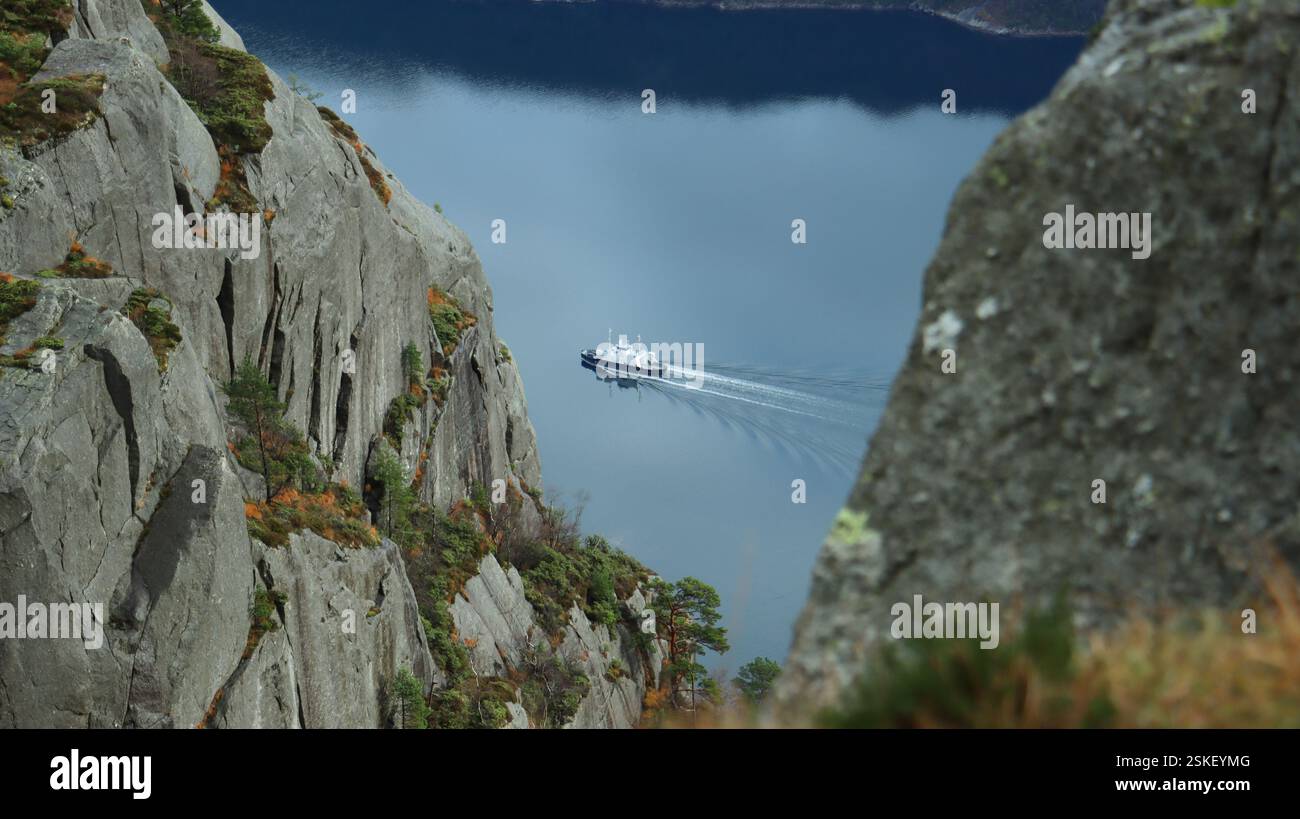 from the top of a cliff we watch a ferry passing through a quiet fjord ...