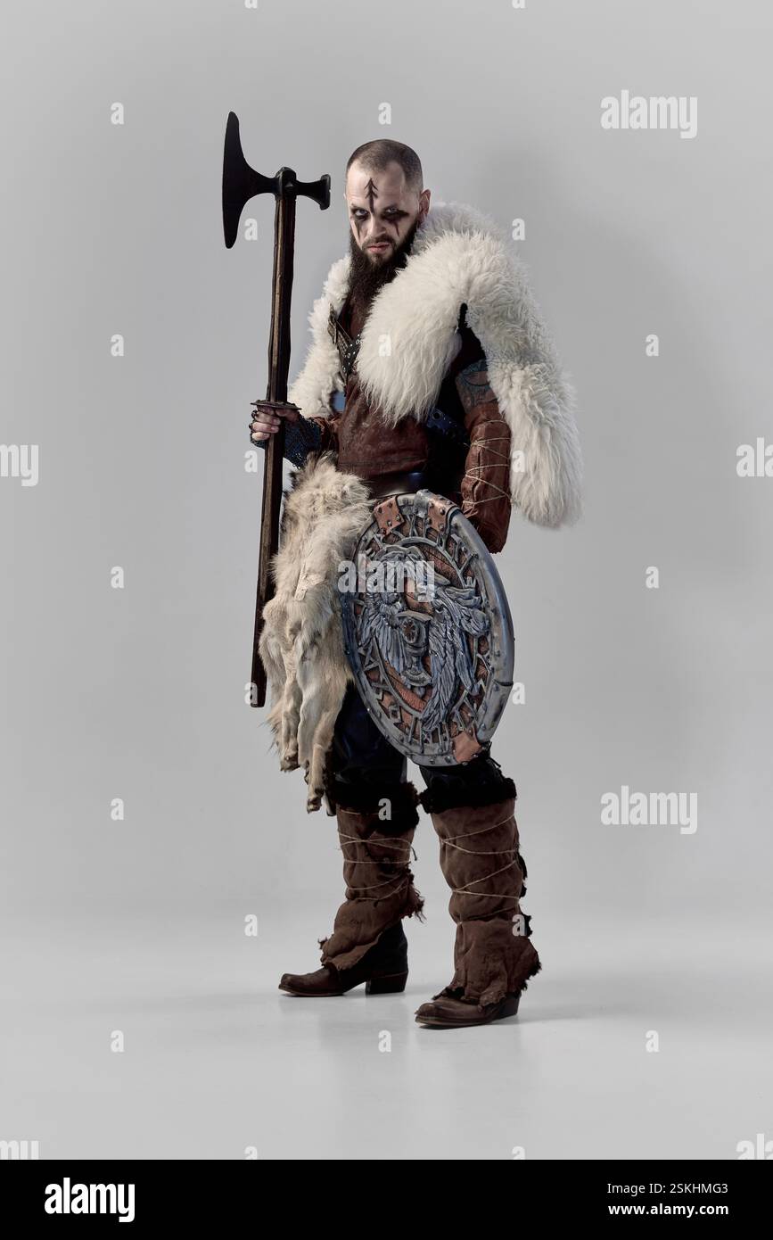 Full-length portrait of medieval Viking, warrior dressed in fur cloak and leather armor, with ...