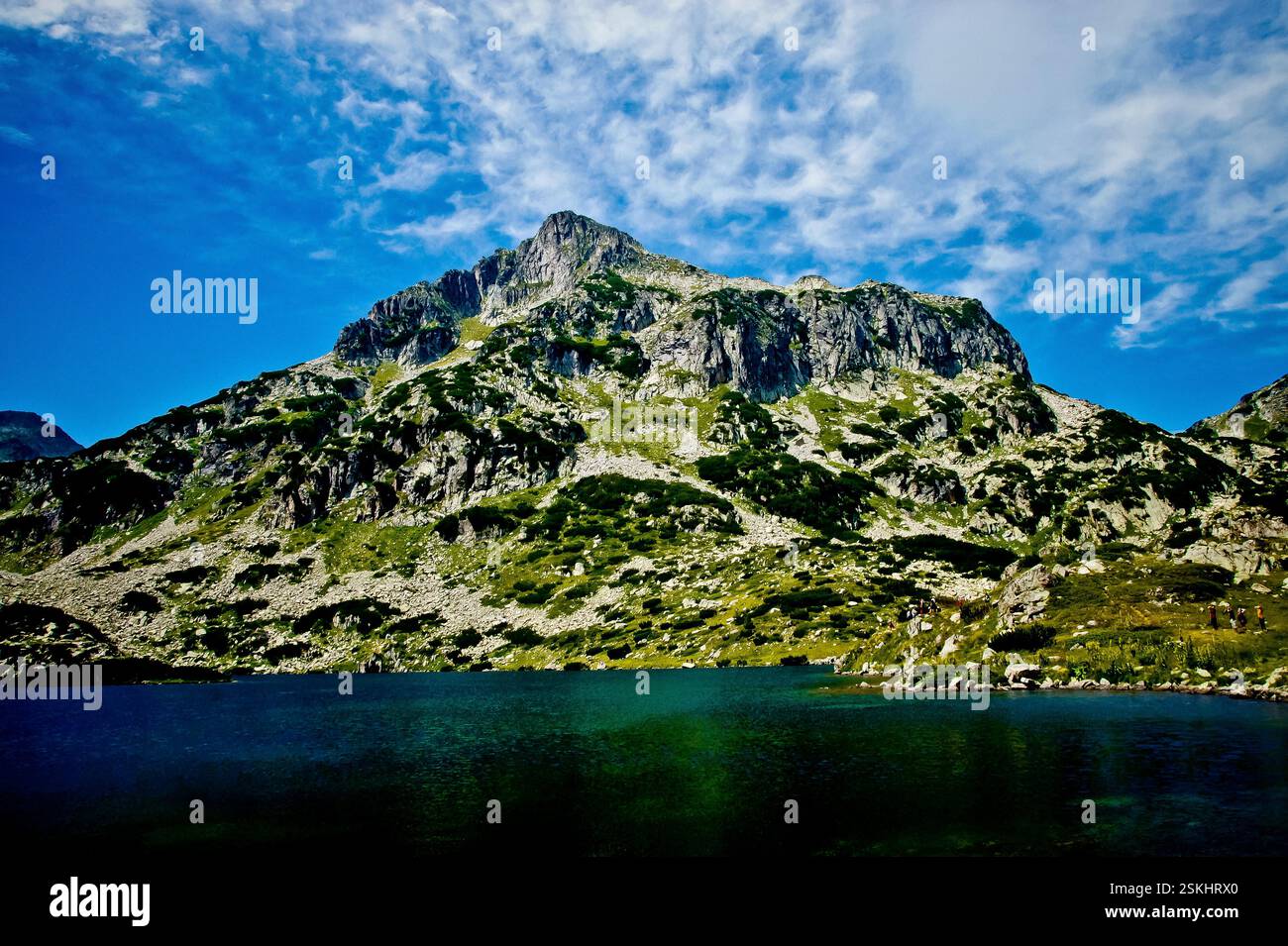 BULGARIA: Mountain. Rugged peak with lush greenery. Calm lake reflects ...