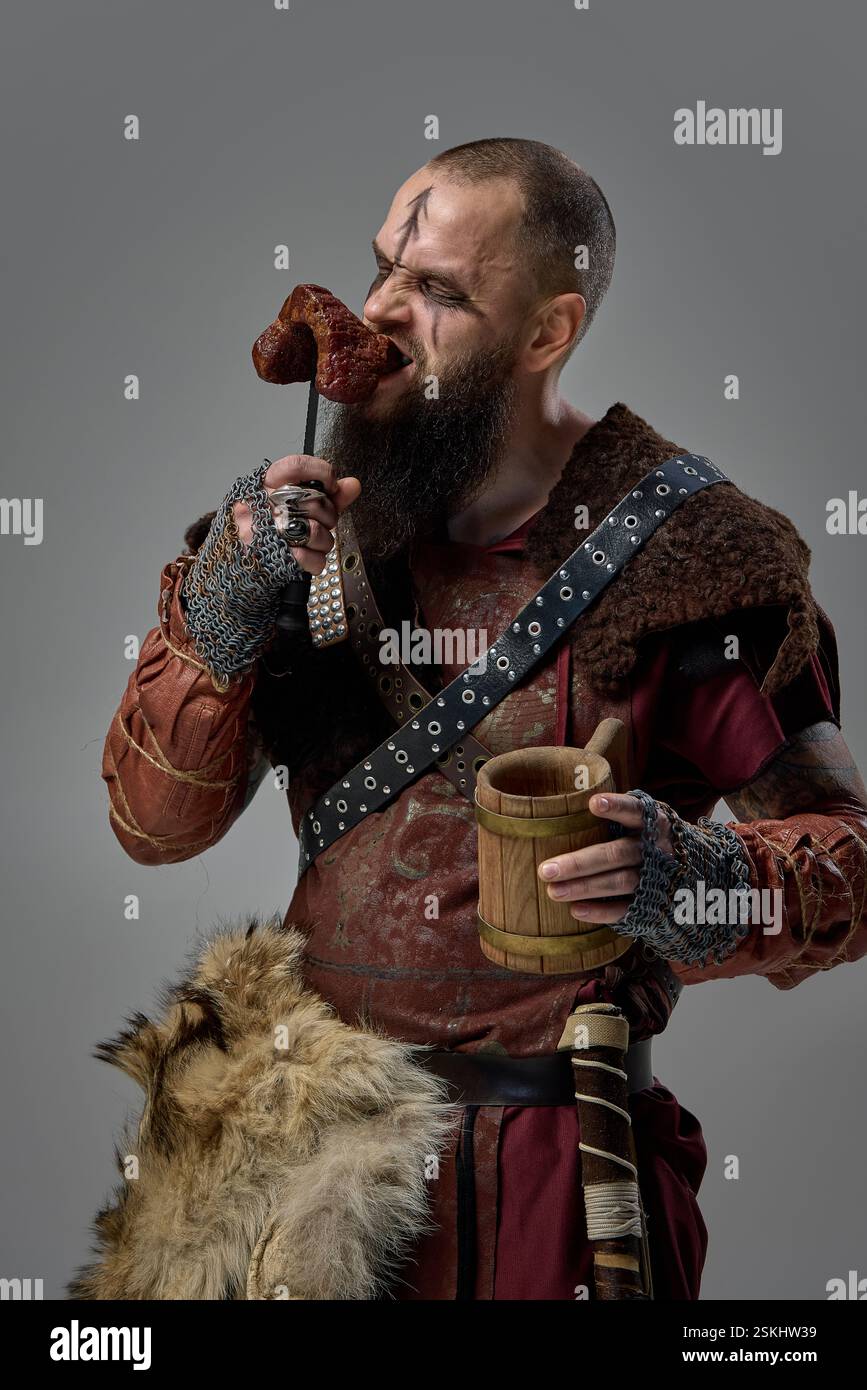 Fierce Viking warrior wearing leather and fur armor biting roasted meat ...