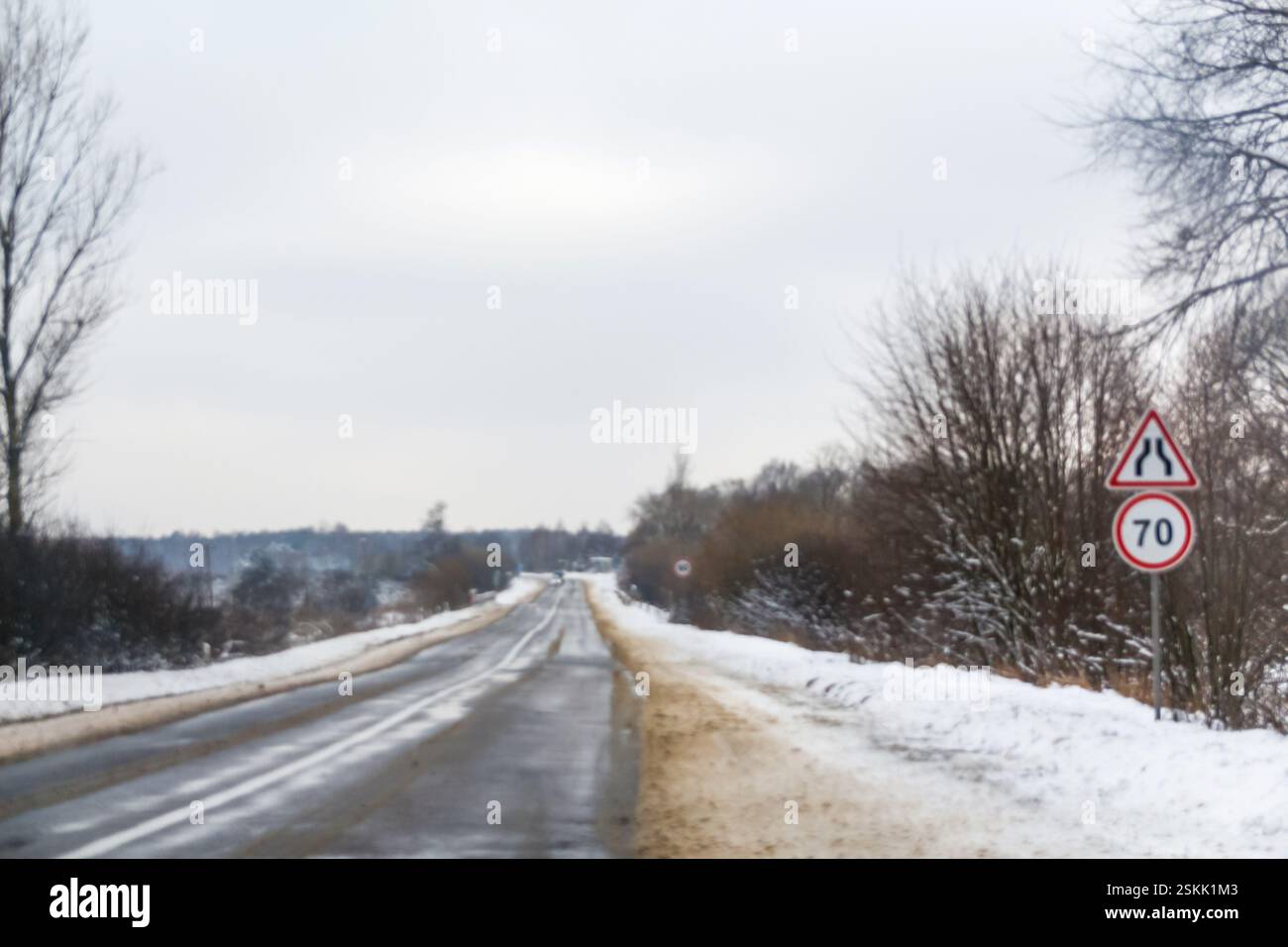 Slippery road warning sign covered in frost, standing against a cold ...