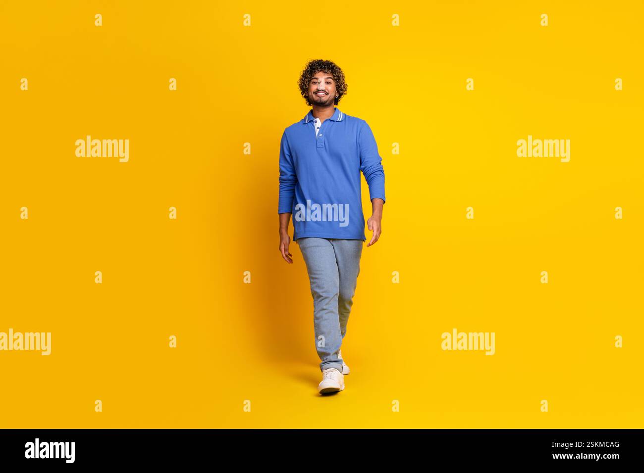 Smiling young man walking confidently against a vibrant yellow backdrop ...