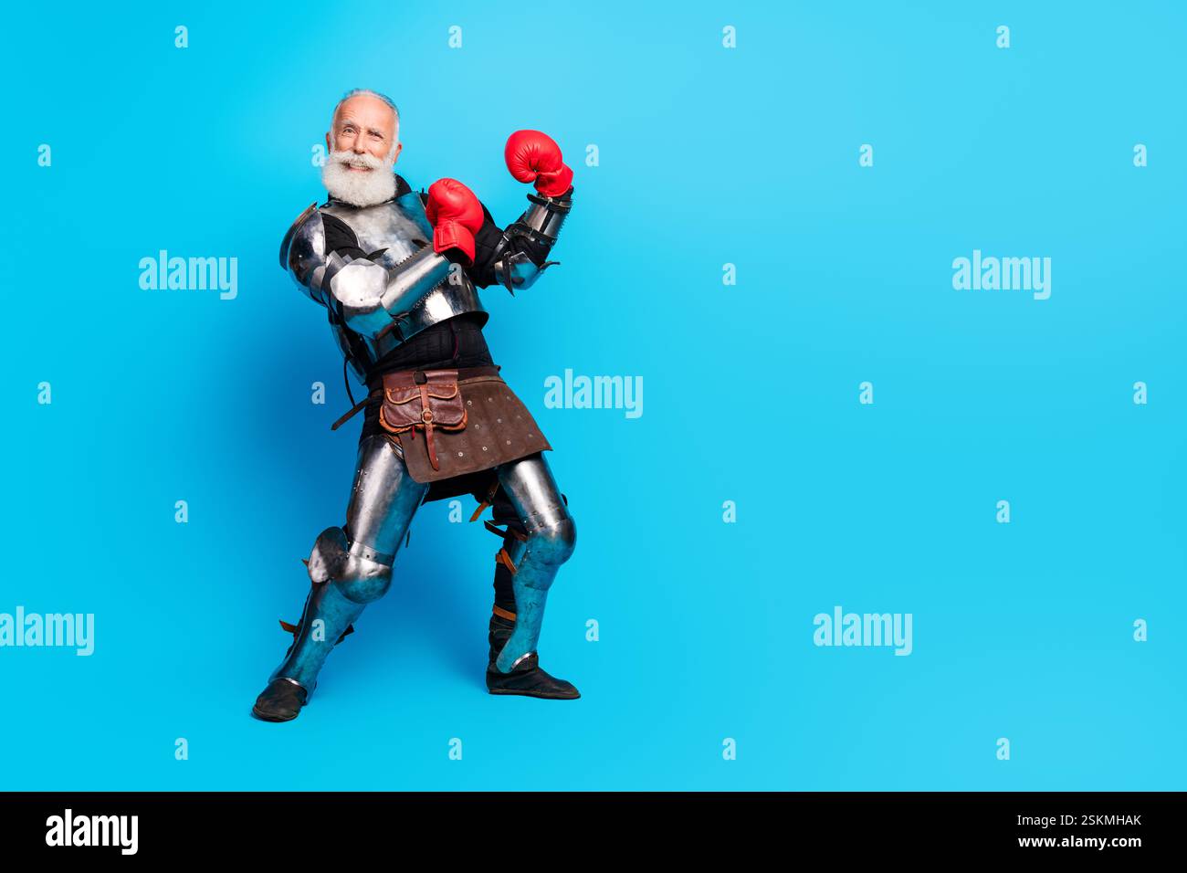 Elderly man dressed as a knight with boxing gloves posing against a ...