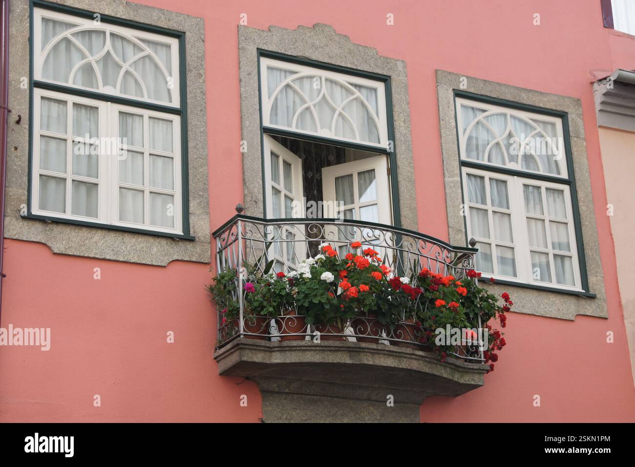 Vibrant geraniums cascade from a wrought iron balcony, framed by ...