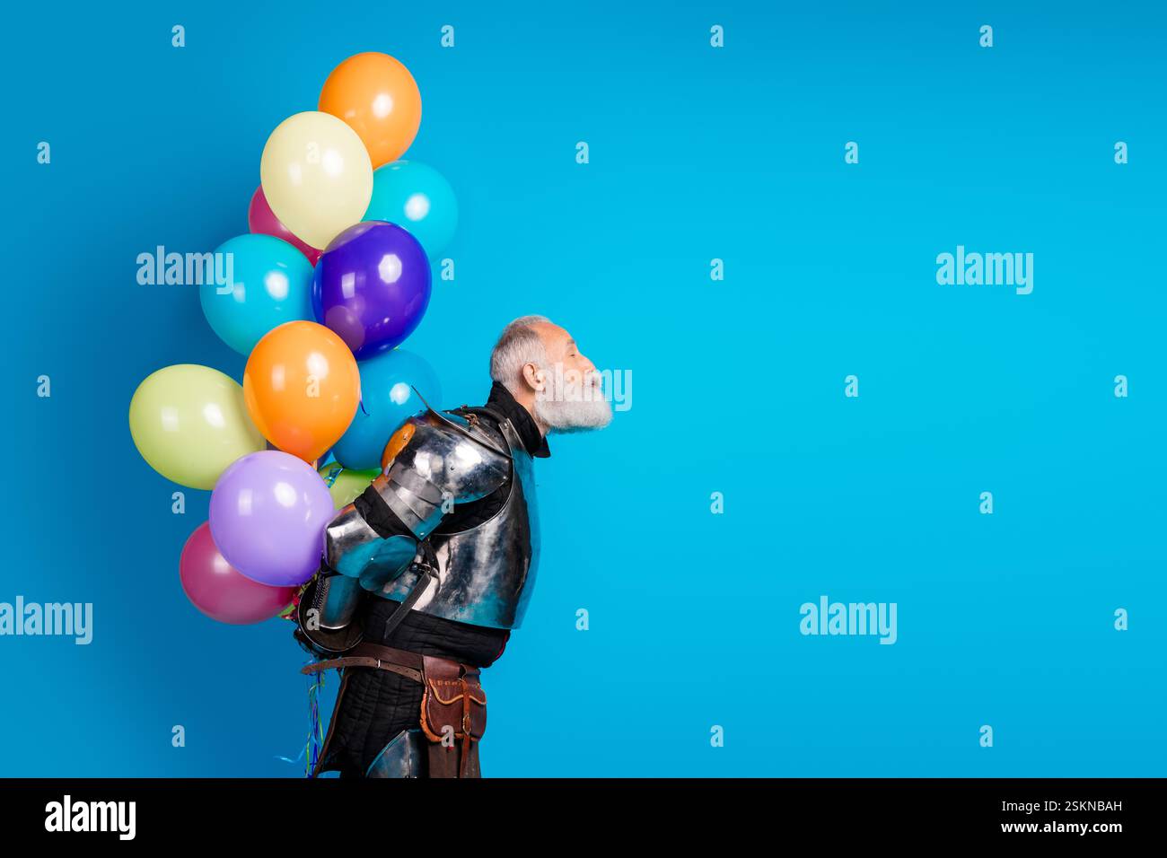 Elderly man dressed in medieval knight armor holding colorful balloons ...