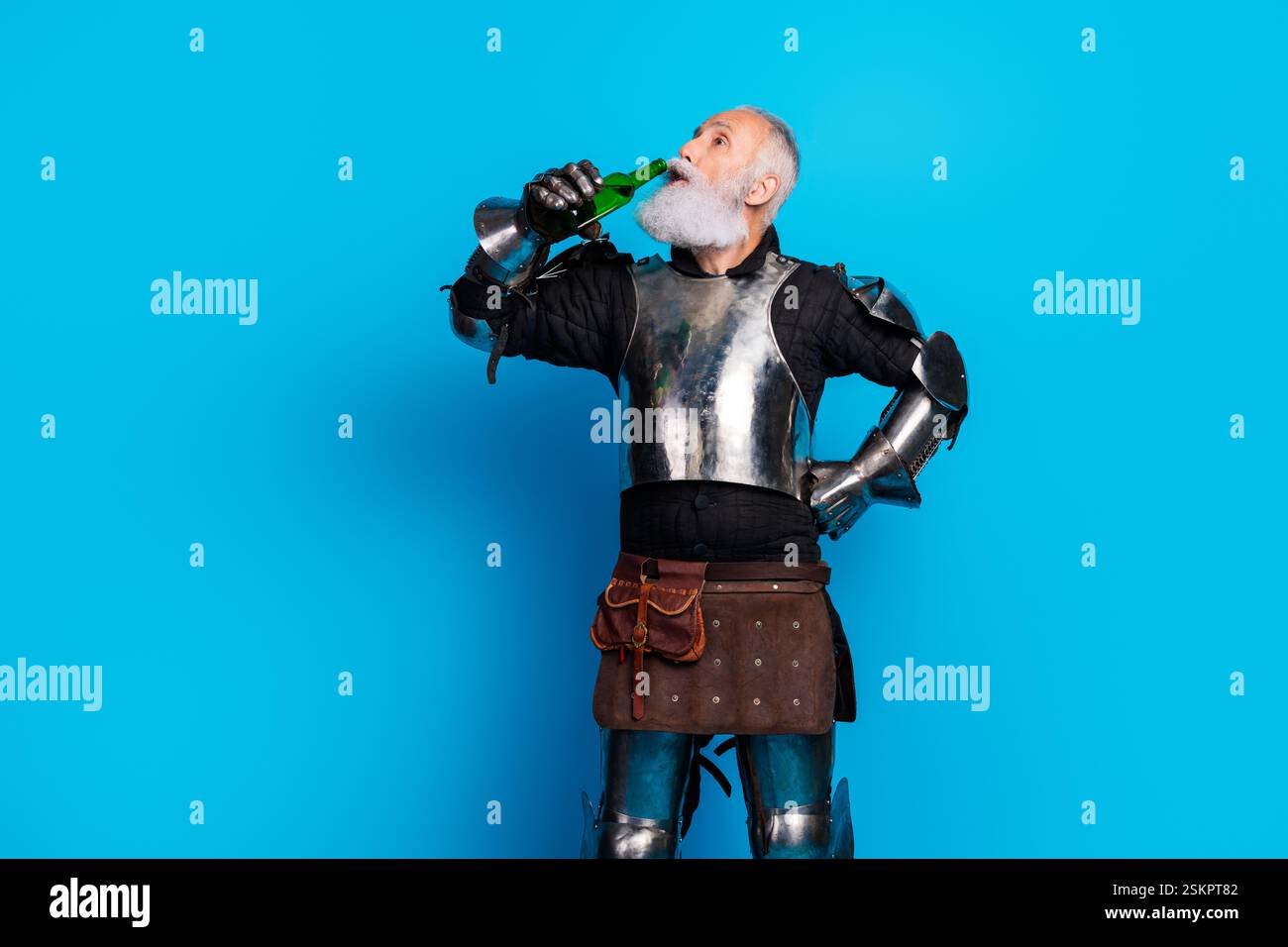 Elderly man in medieval knight armor enjoying a drink against a bright ...